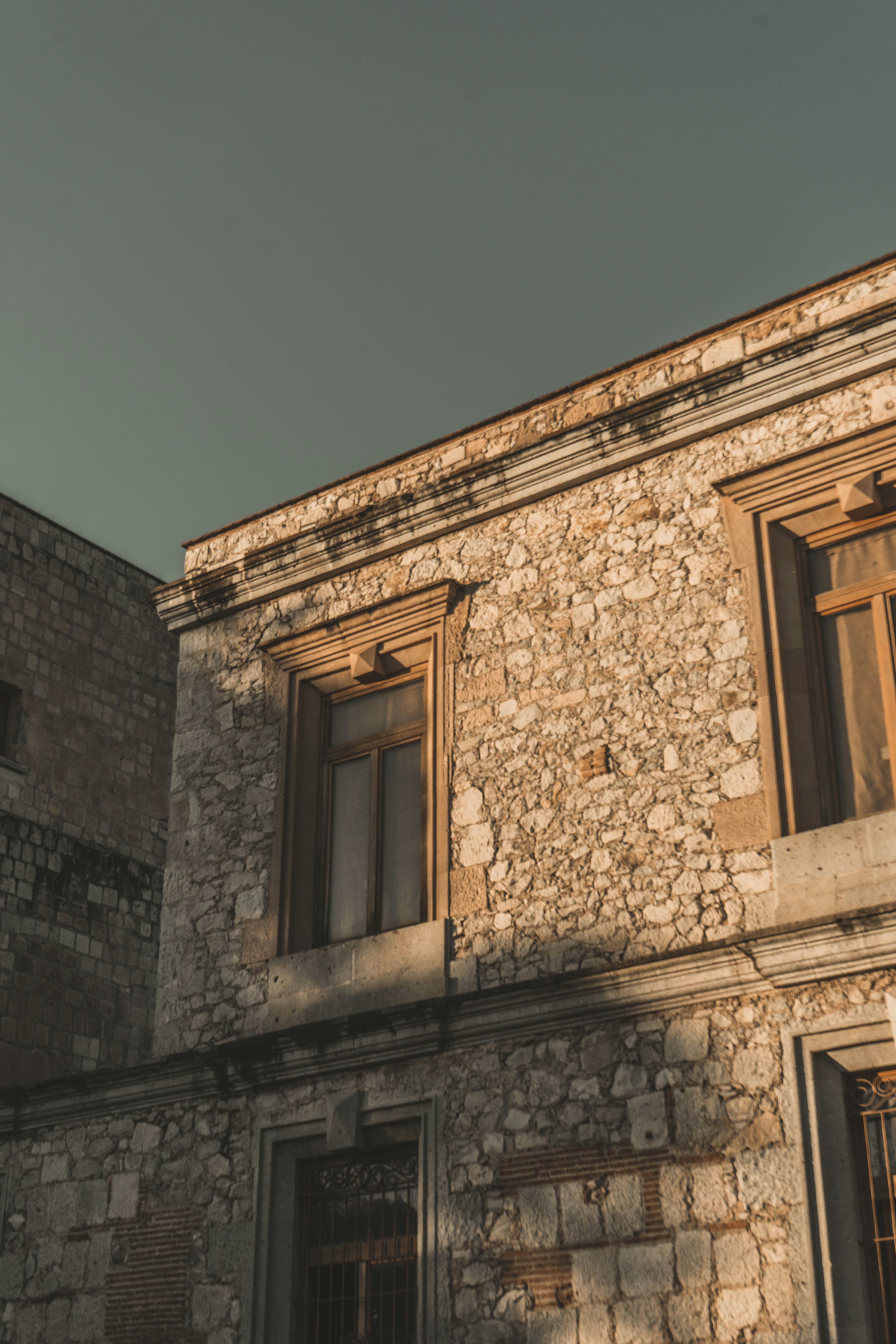 Weathered stone building with ornate windows, bathed in warm sunlight, showcasing architectural details from a bygone era.
