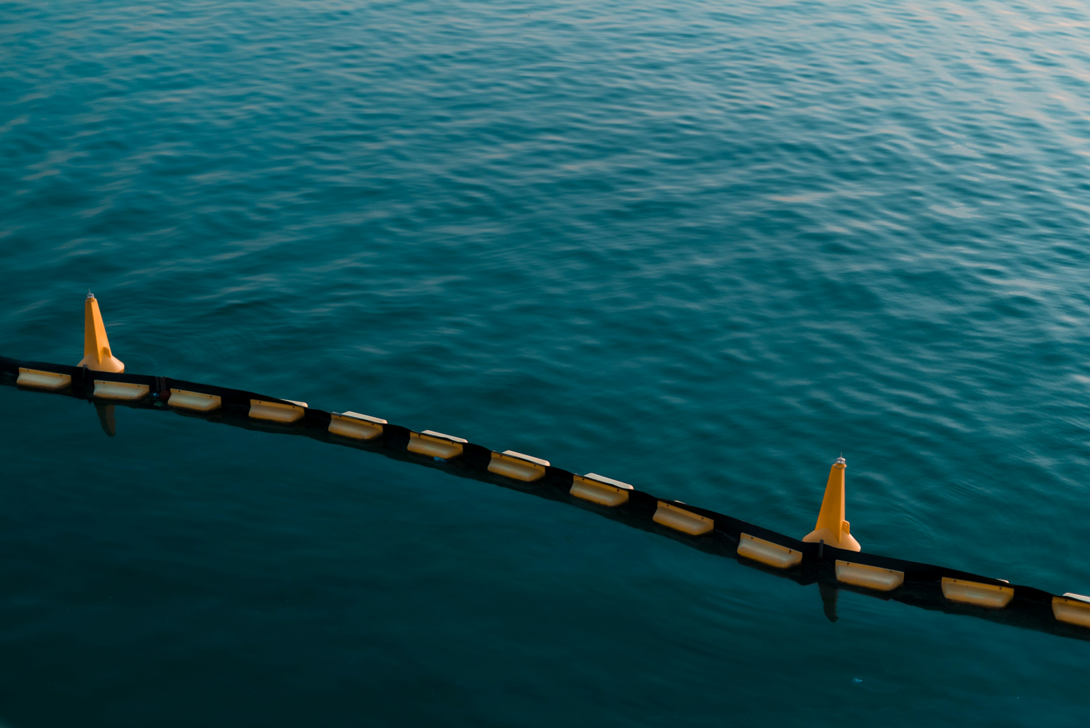 A curved floating barrier with yellow buoys contrasts against the tranquil blue water surface, illustrating a division in aquatic space.