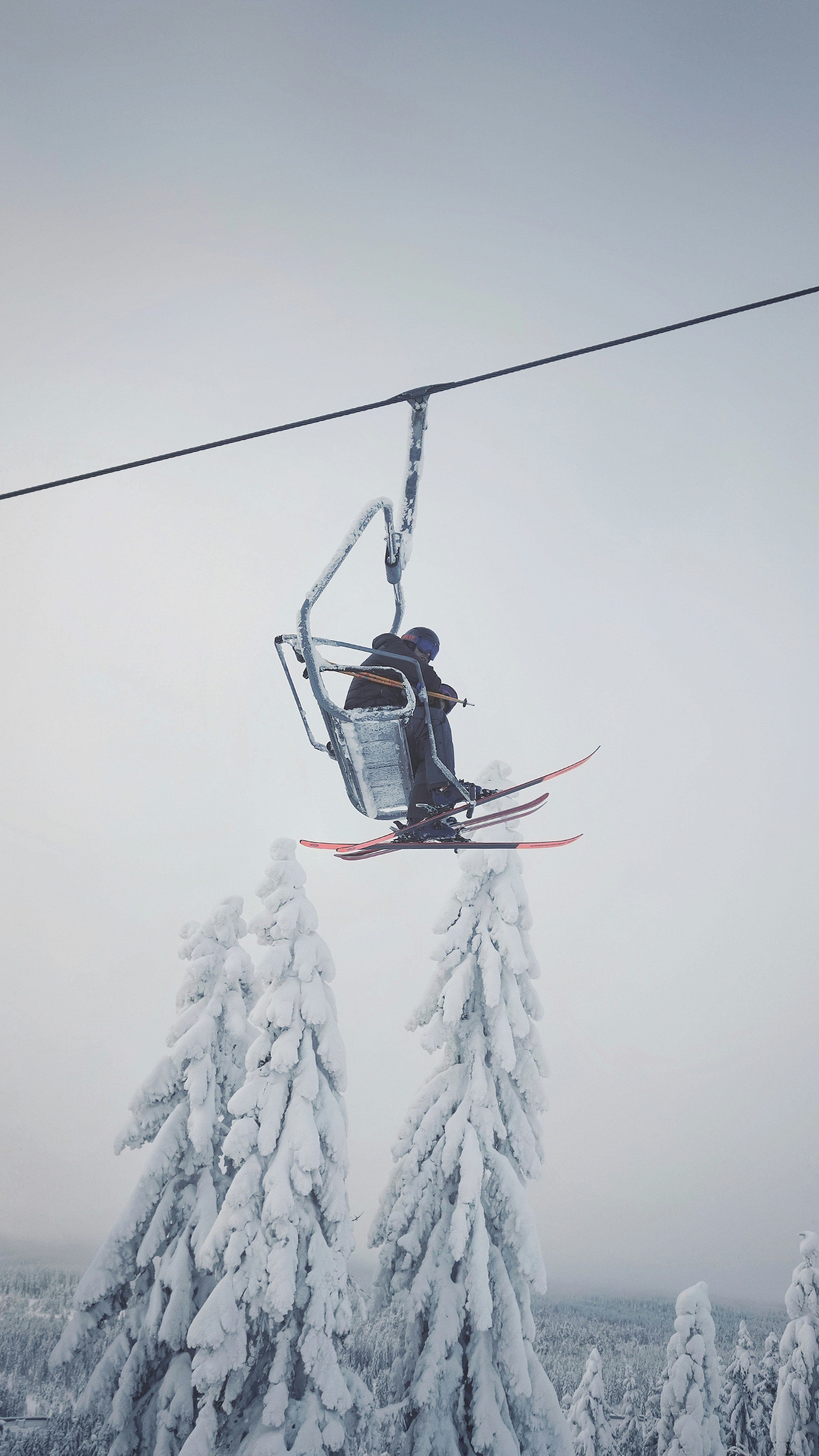 A skier rides a chairlift above snow-covered trees, surrounded by a serene winter landscape.