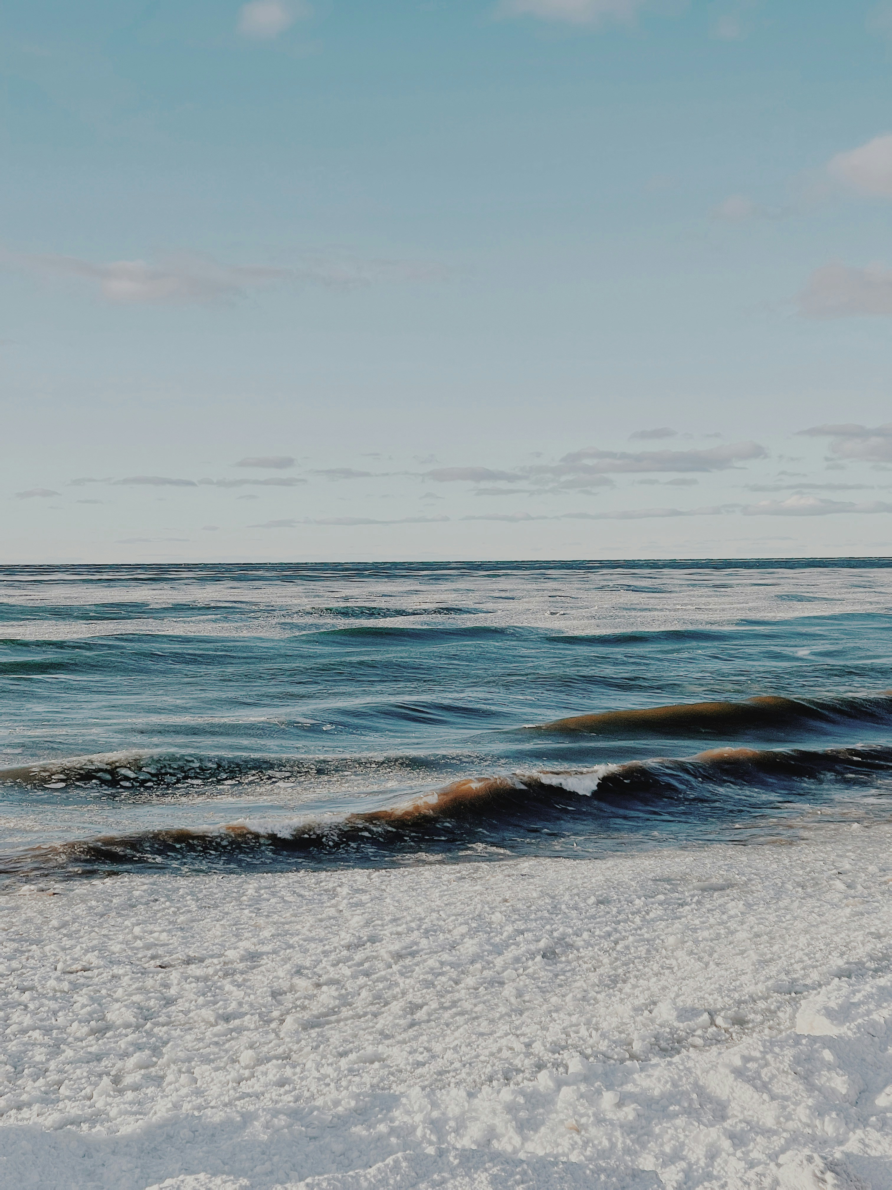 Gentle waves lapping against a snowy shoreline under a clear blue sky.