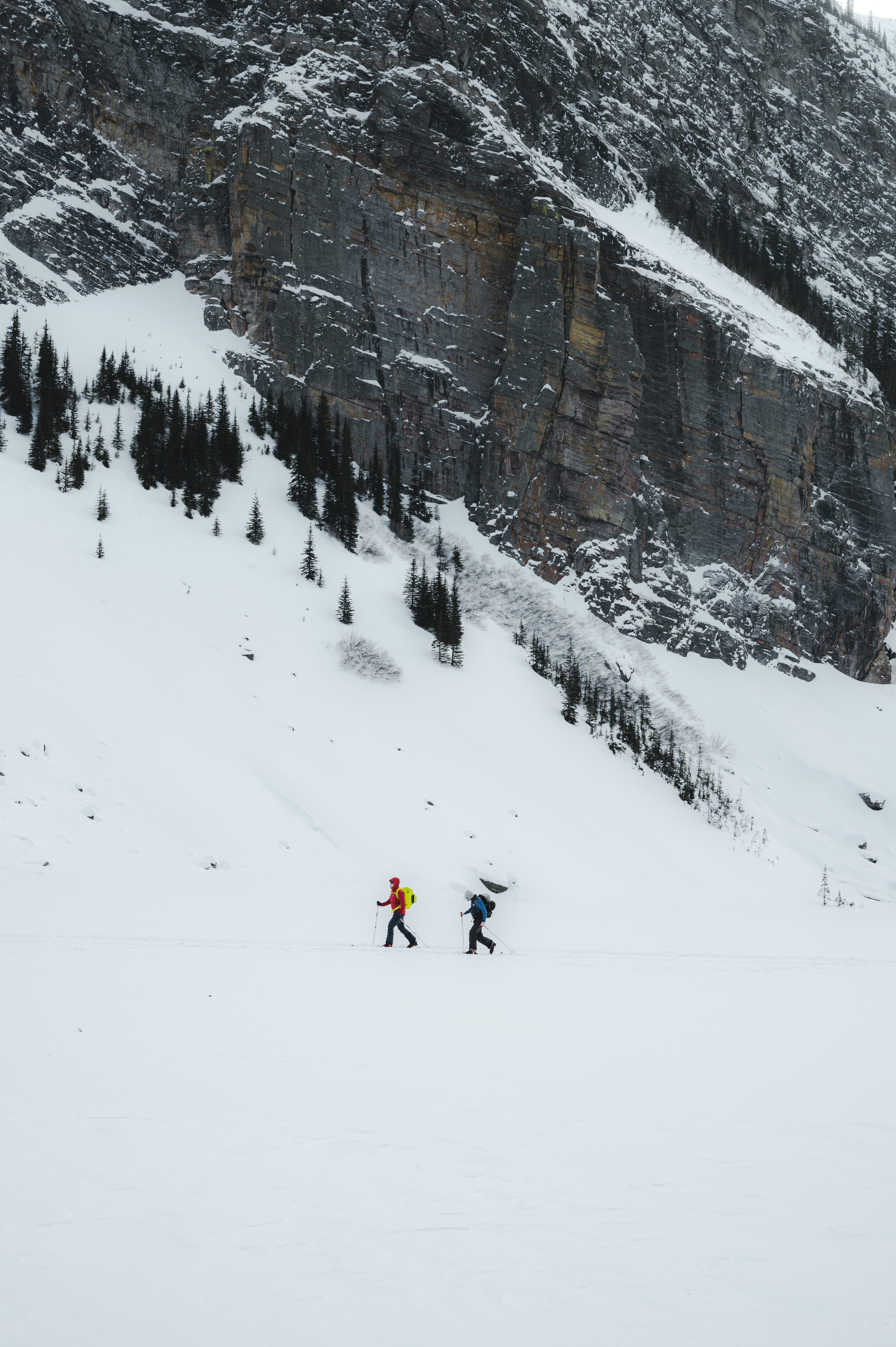 Two climbers carve a quiet track across a snowfield beneath a cliff