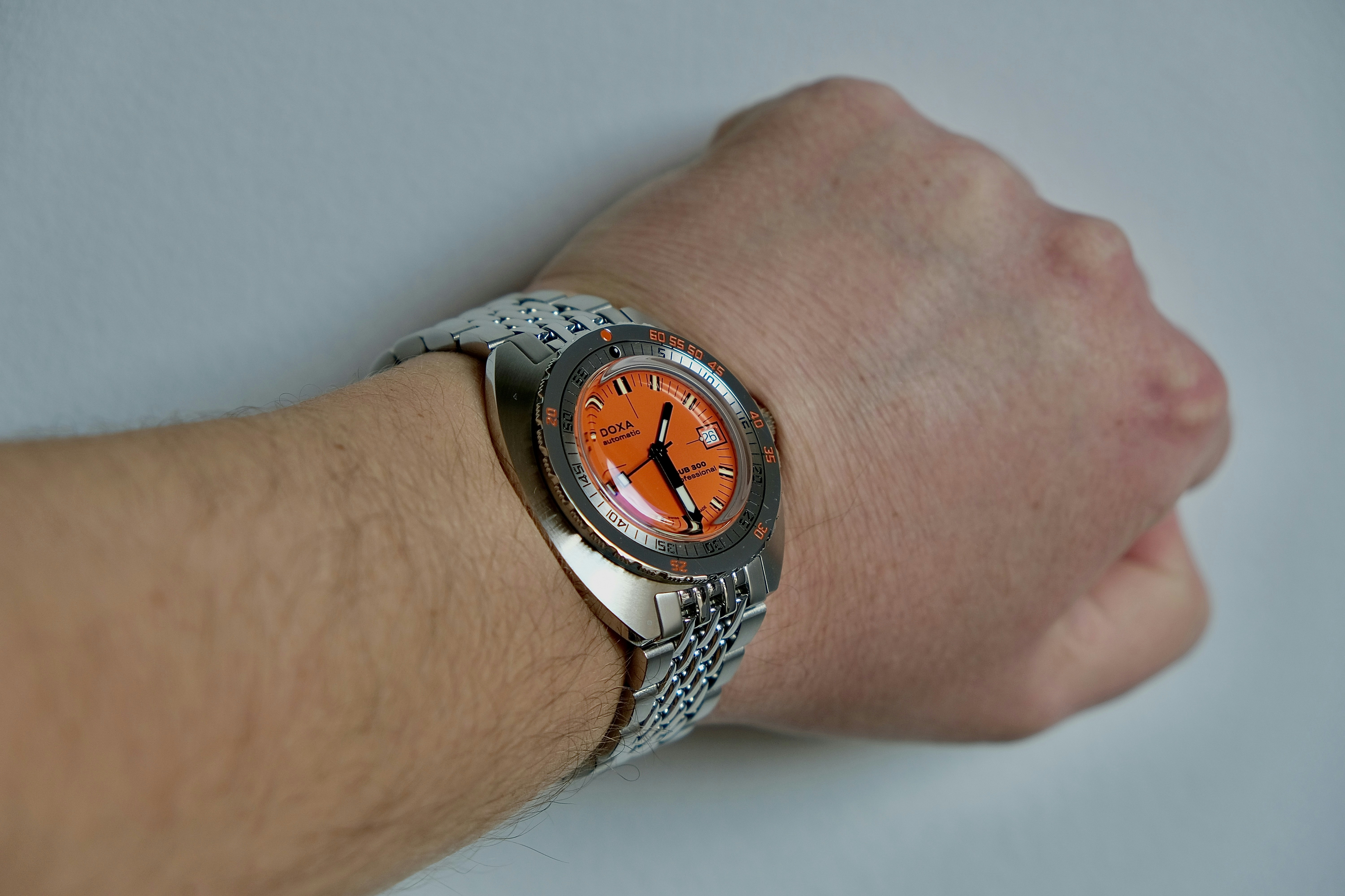 A stylish wristwatch featuring a striking orange dial and silver mesh band, showcased against a neutral backdrop.