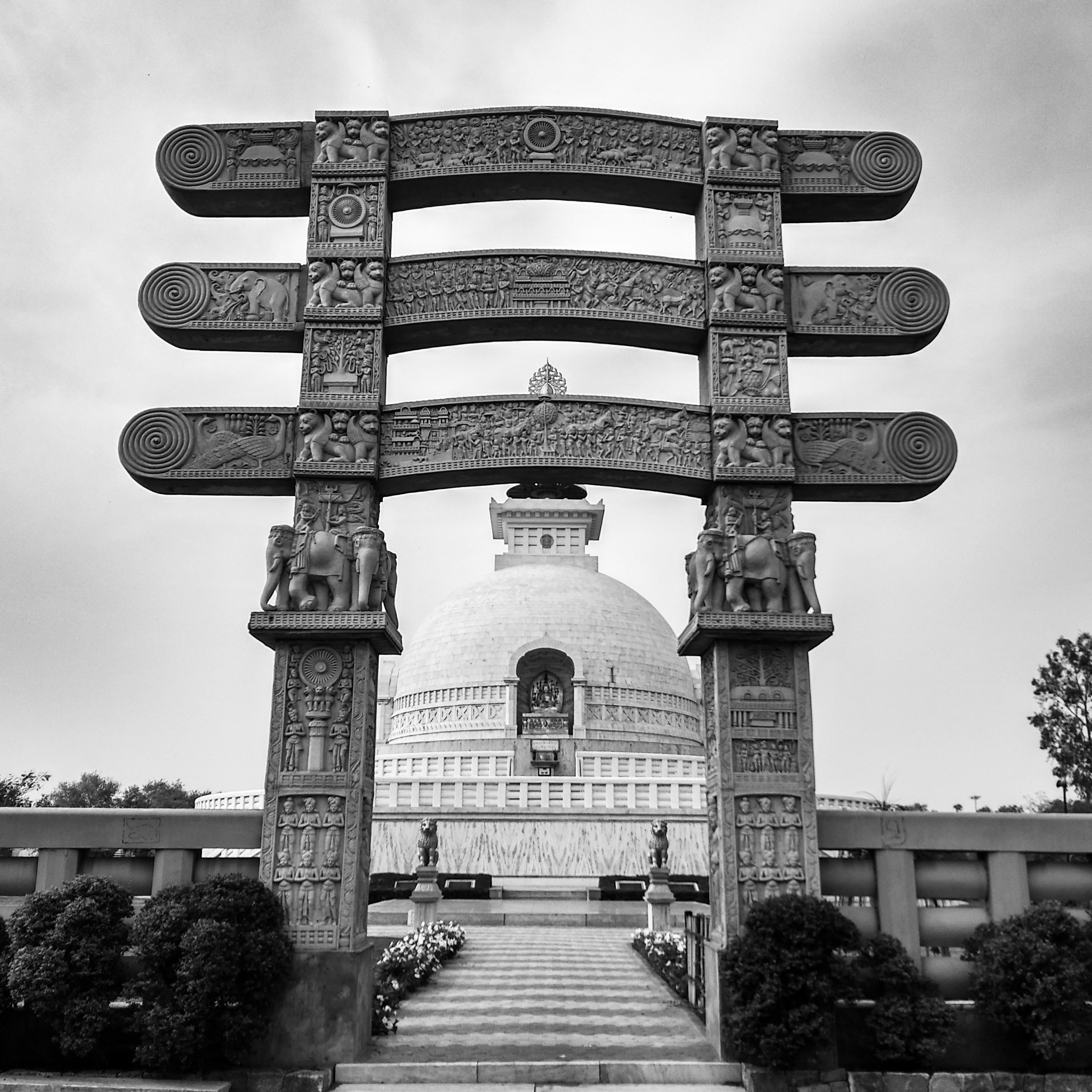 Intricate stone gateway framing a large stupa, showcasing detailed carvings and serene surroundings.