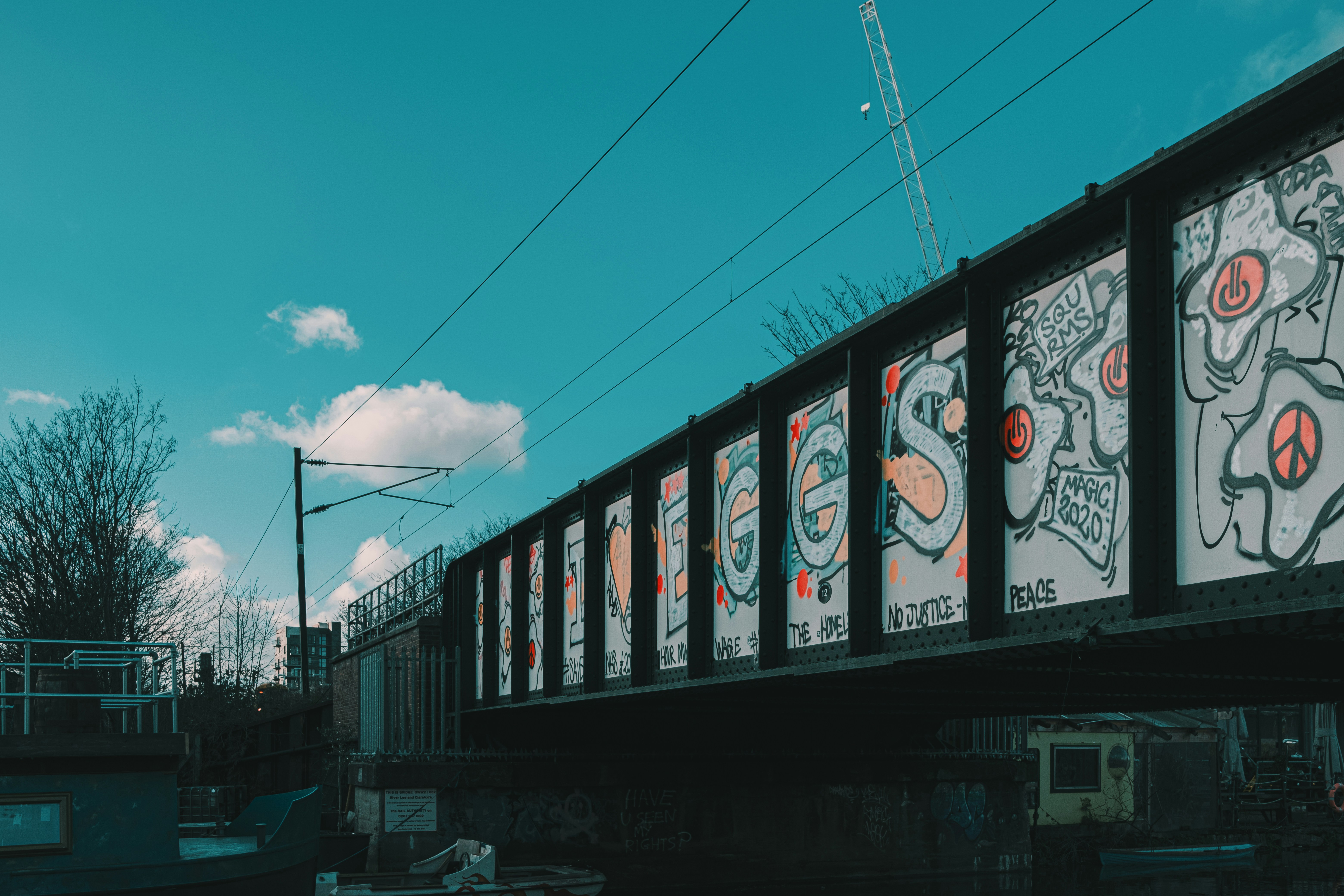 Graffiti-covered railway bridge adorned with vibrant artwork against a bright blue sky with scattered clouds.