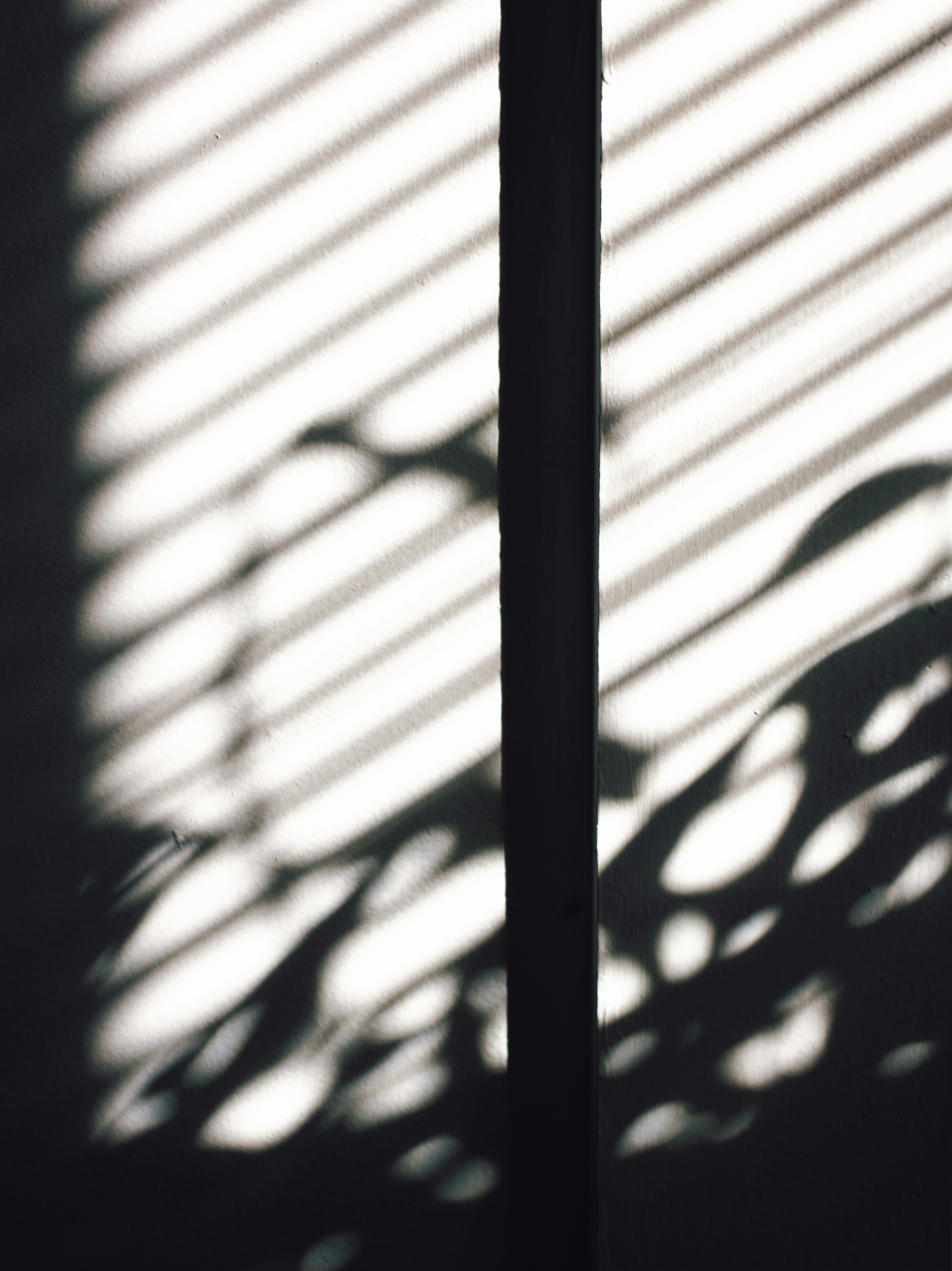 Intricate shadows cast by blinds create a rhythmic pattern on a wall, highlighting the interplay of light and dark.