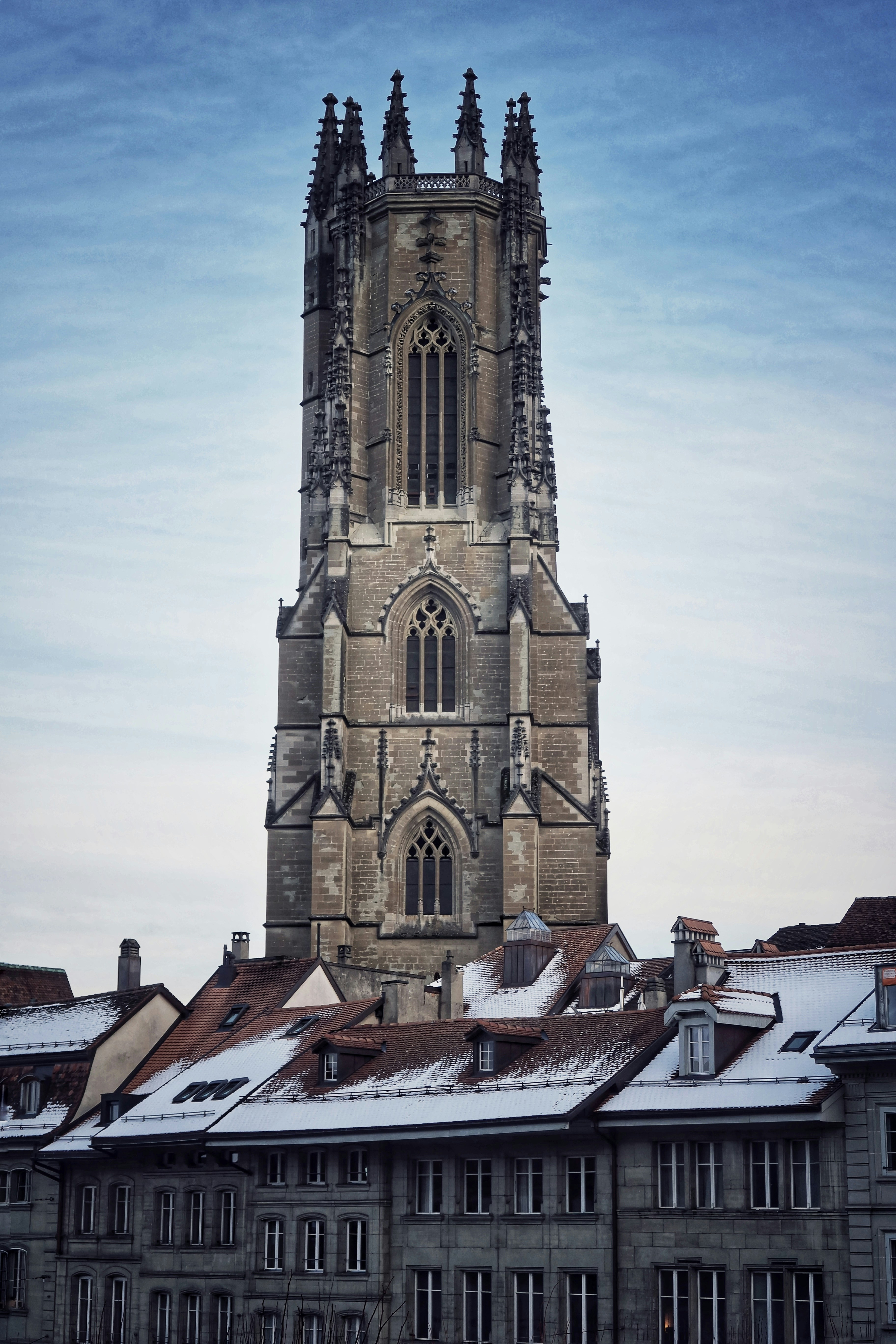 Gothic tower rising above snow-covered rooftops under a serene sky.