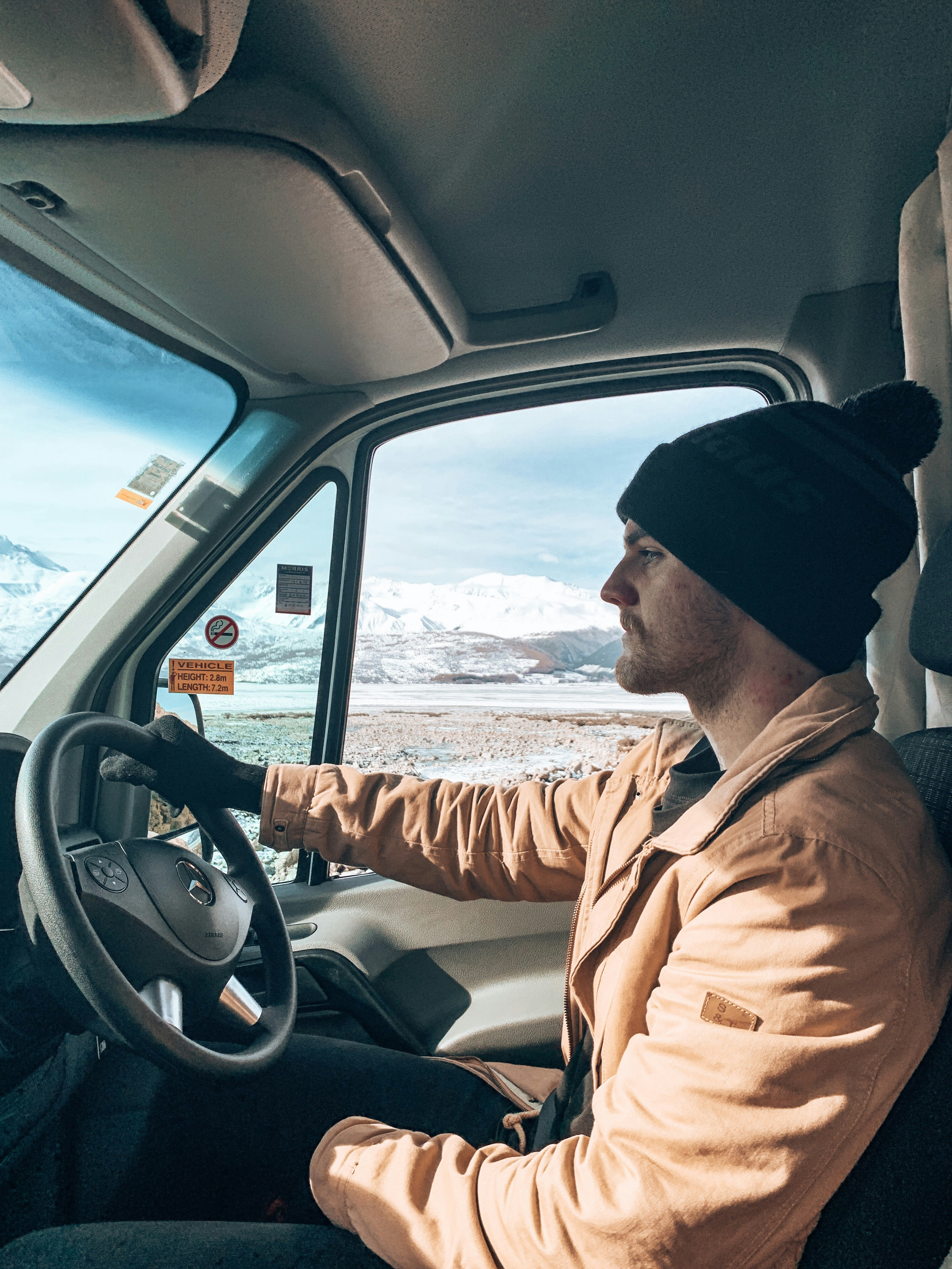 Driver focused on the road with a panoramic view of snow-capped mountains outside the van window.