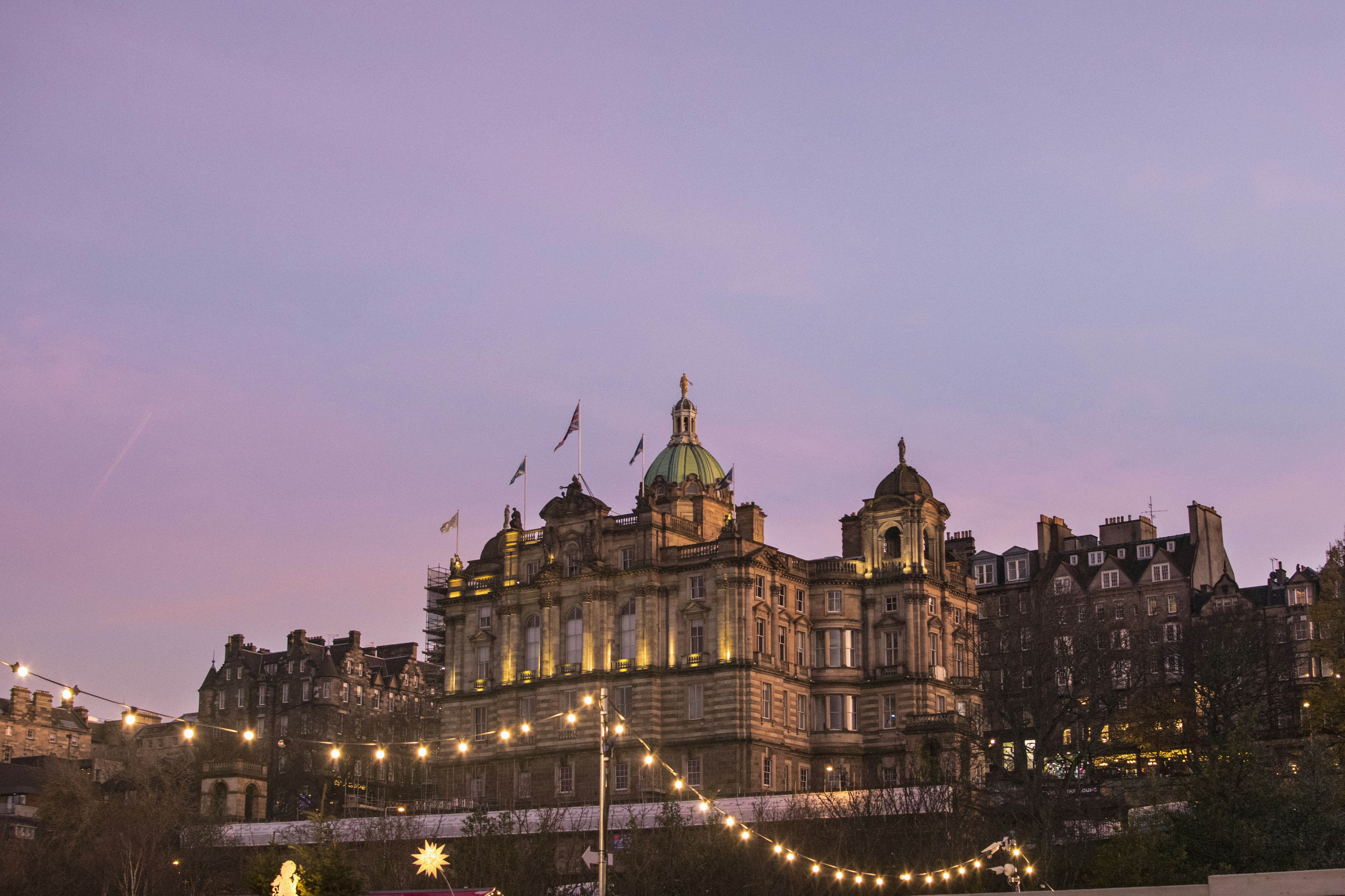 Historic building under a pastel-colored sky with string lights in the foreground.