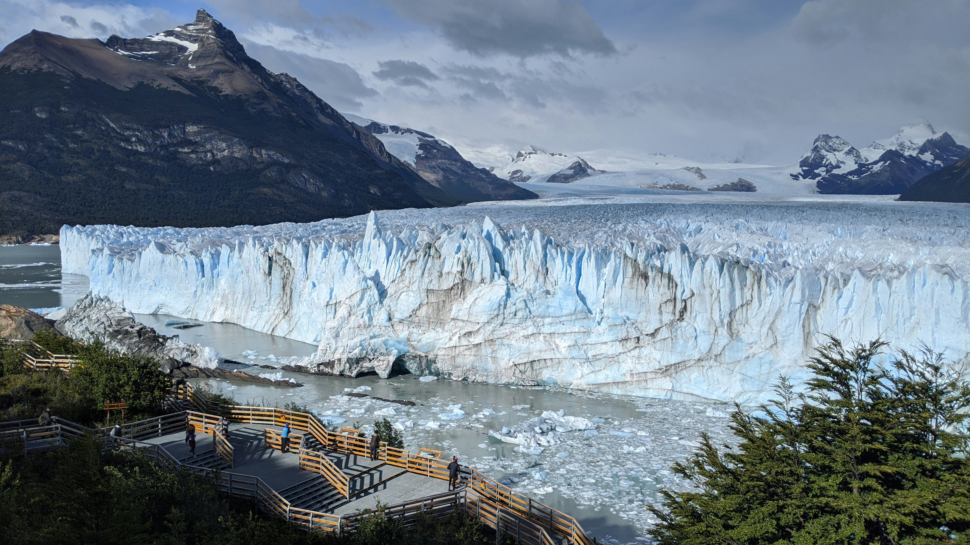 Vast glacier extending between rugged mountains under a cloudy sky.