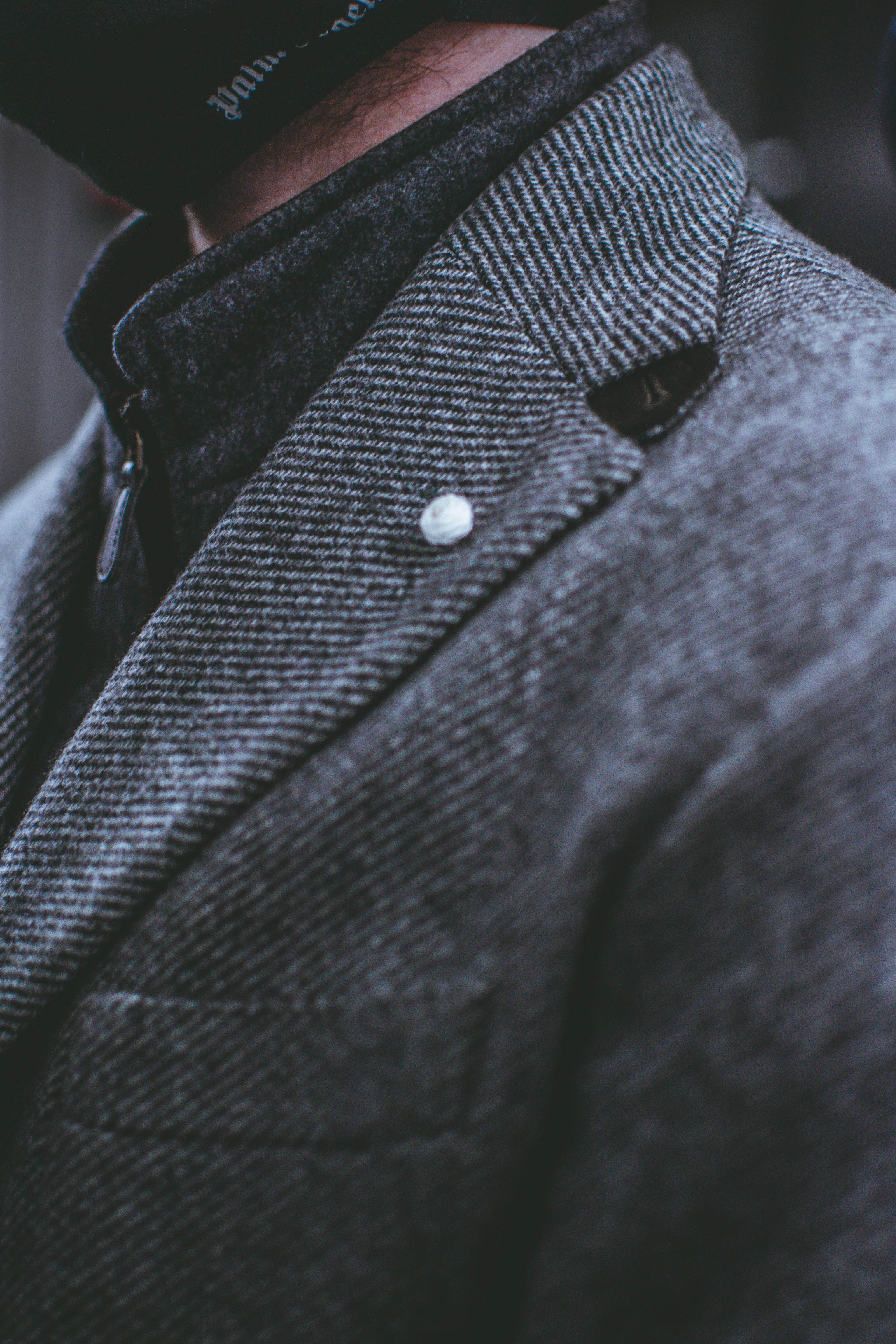 Close-up of a tailored gray herringbone jacket with a visible button, showcasing intricate fabric details and craftsmanship.