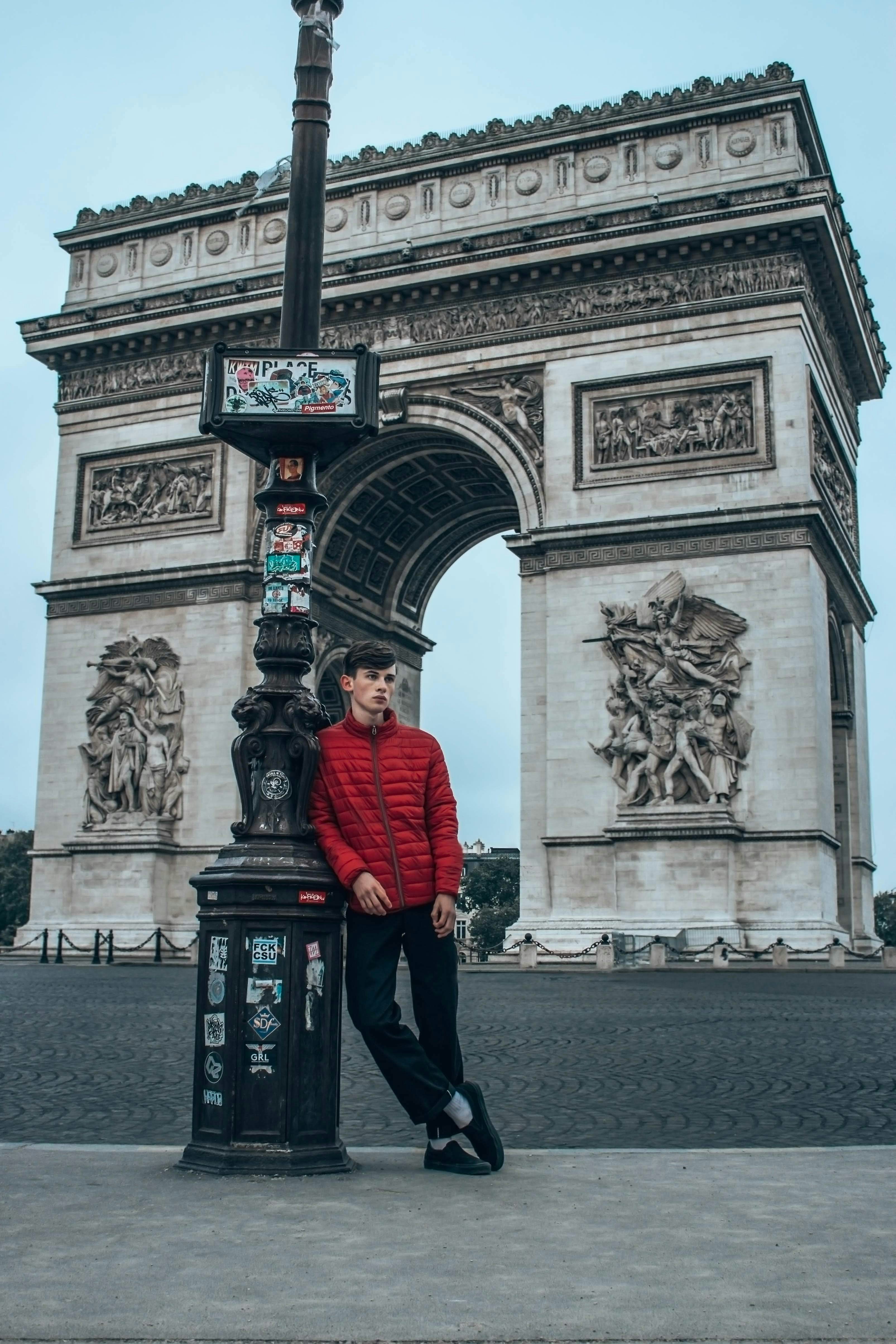 Red Jacket at the Arc de Triomphe: A quiet stance by a stickered lamppost