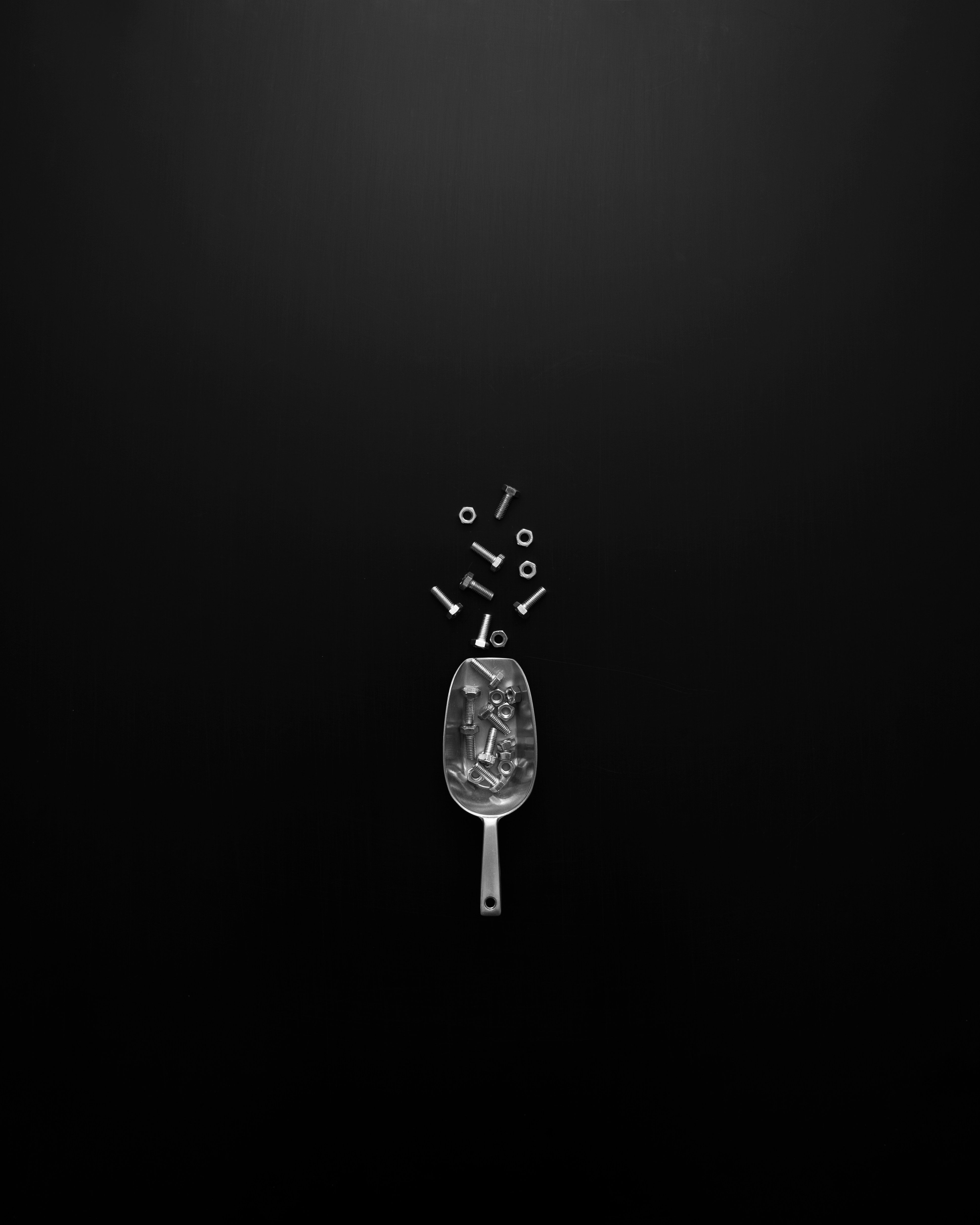 A silver spoon cradles scattered metal fasteners against a stark black backdrop, emphasizing the contrast between form and function.