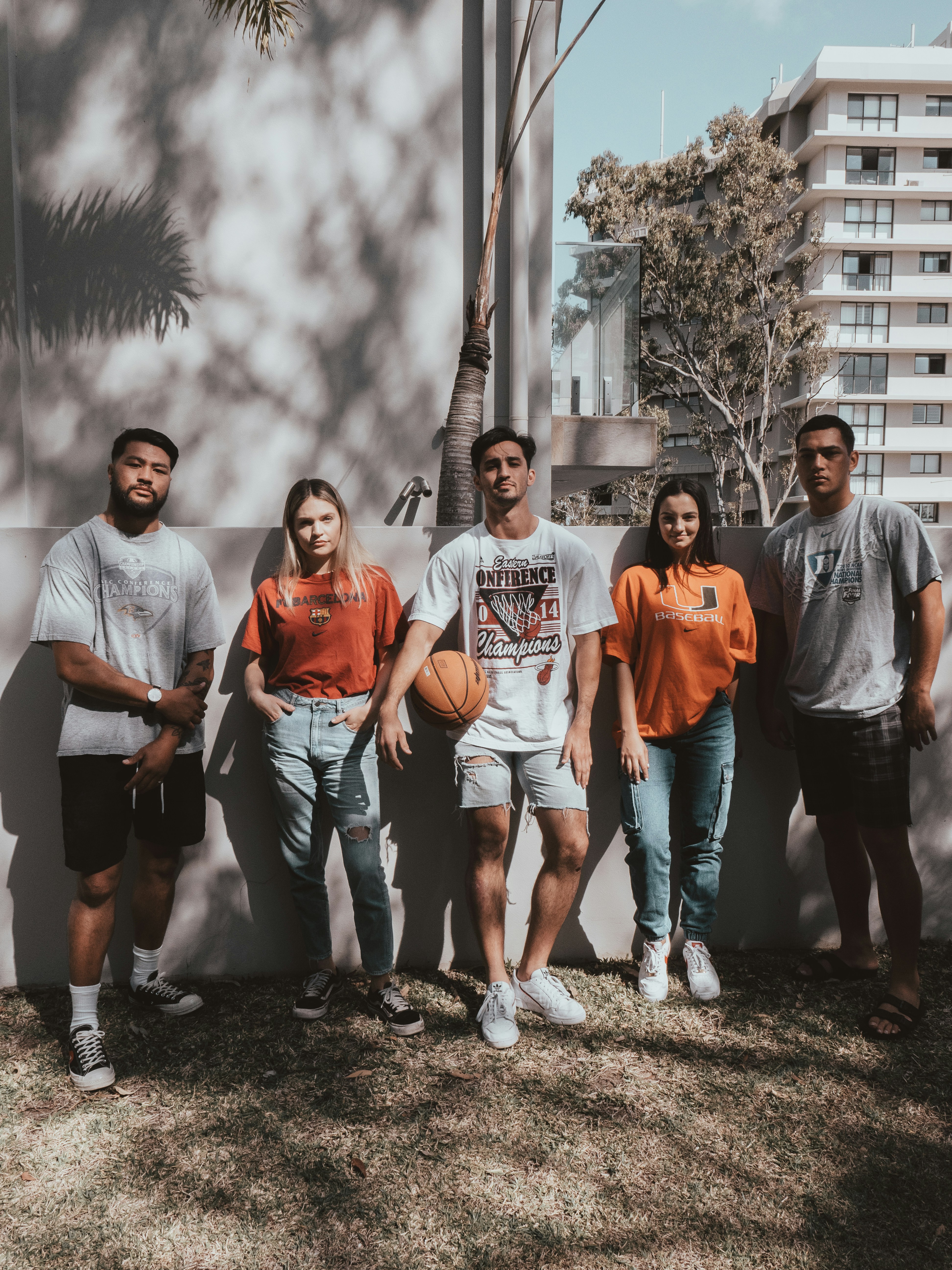 Group of five friends posing together outdoors, with one holding a basketball, showcasing a casual and sporty vibe.