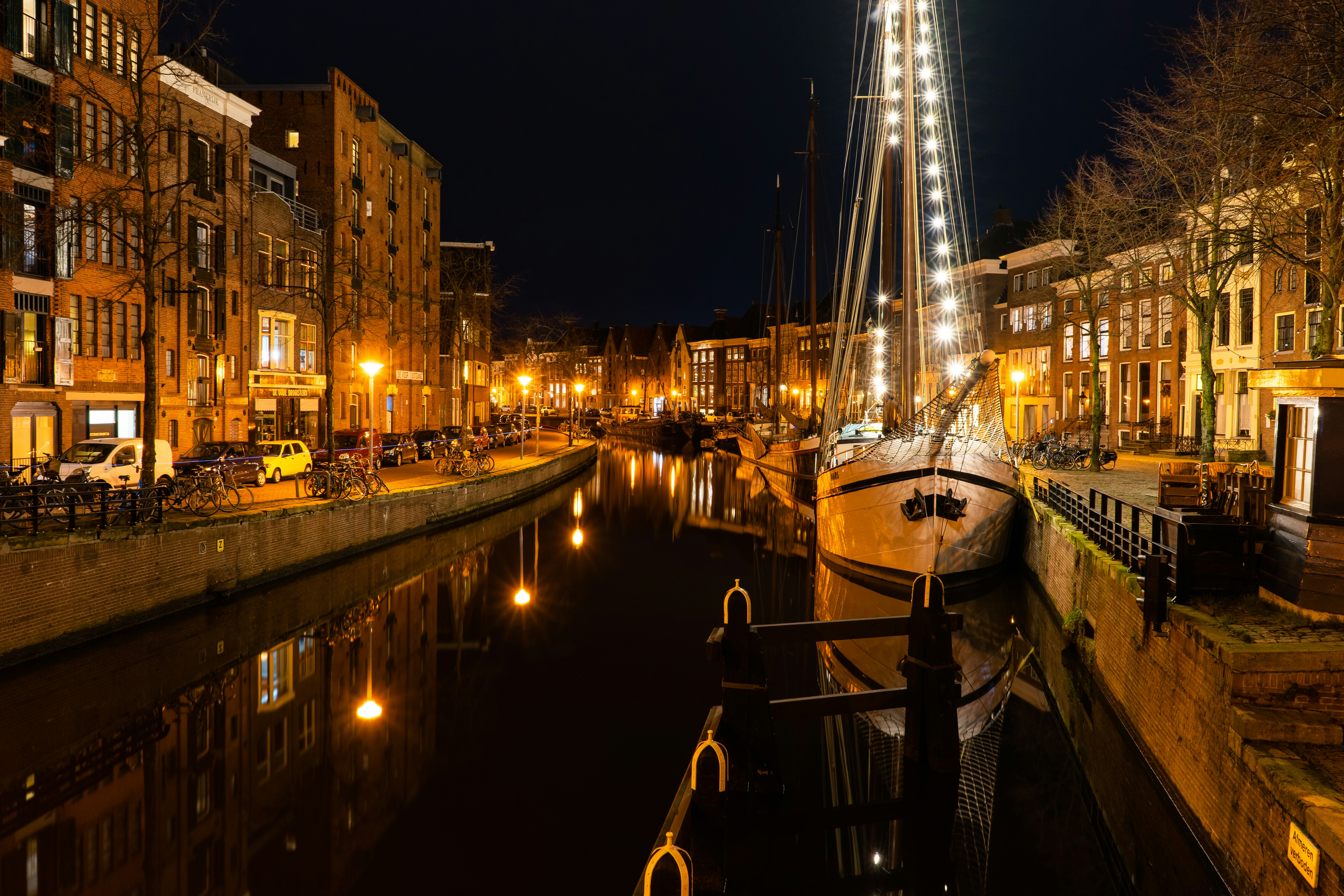 Illuminated boat docked along a canal, surrounded by warmly lit buildings at night.