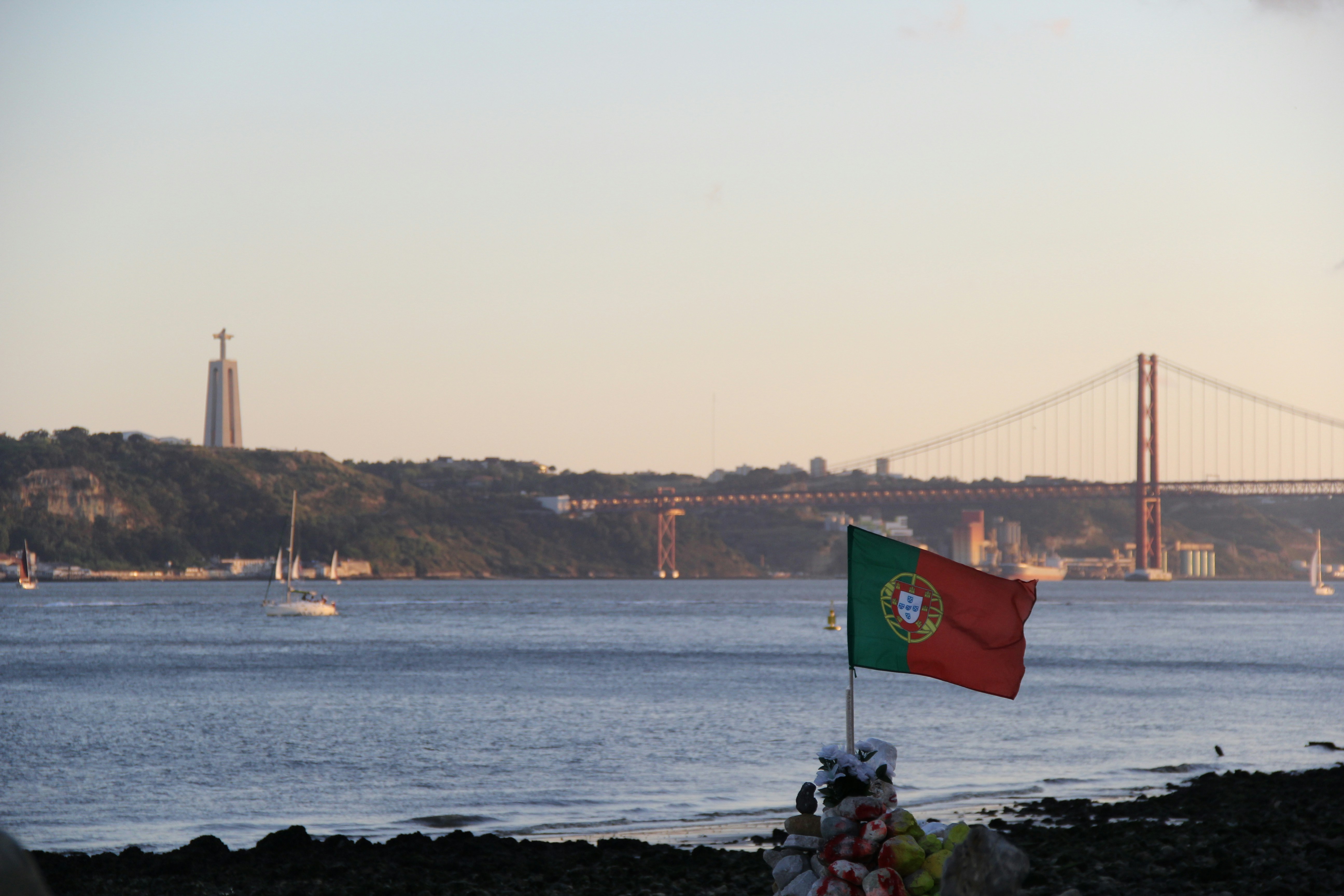 Portuguese flag waving in the foreground with the iconic 25 de Abril Bridge and Cristo Rei statue in the background, symbolizing Lisbon's rich heritage.
