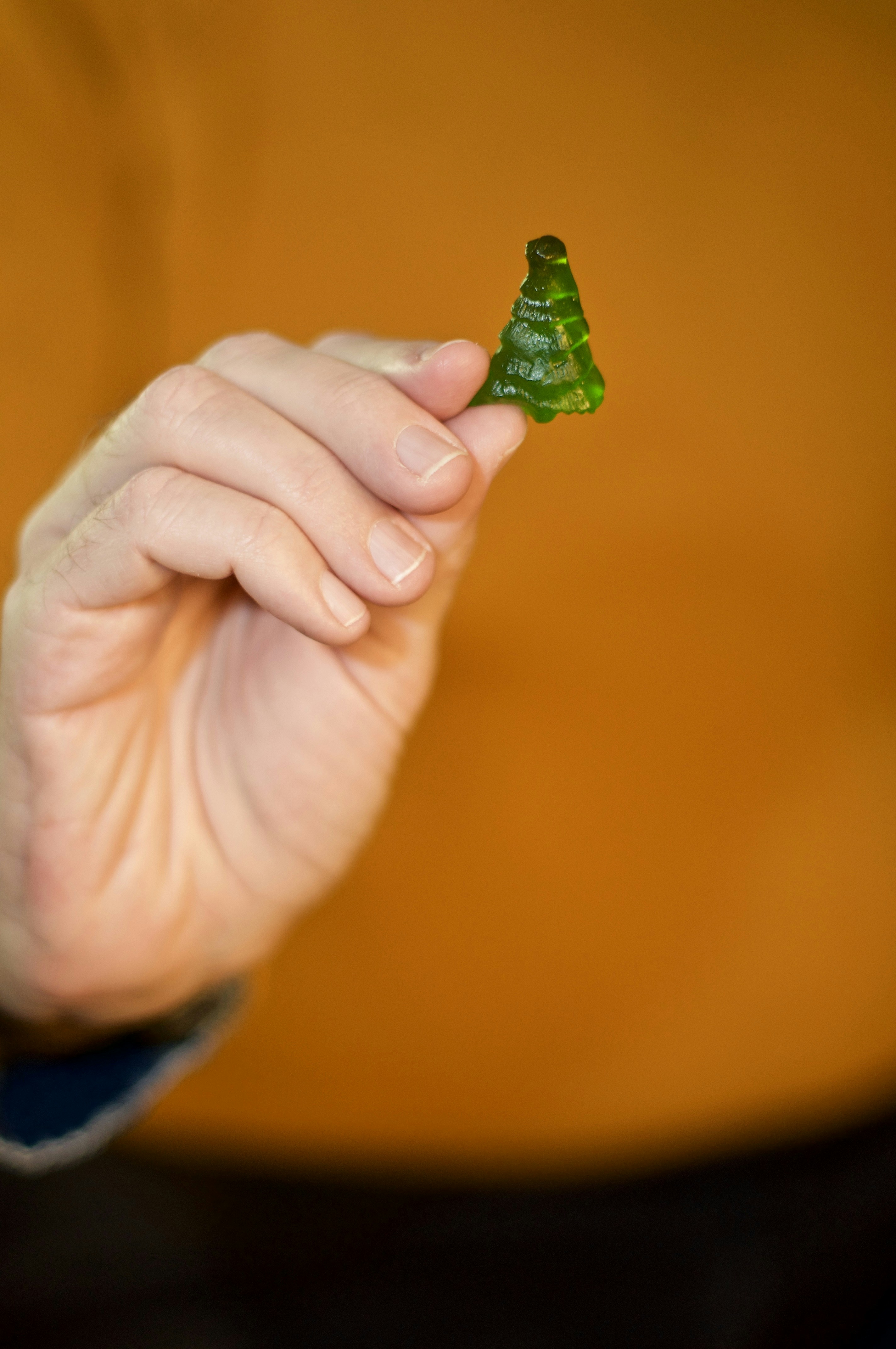 A hand holding a small green candy shaped like a Christmas tree, set against a warm, blurred background.