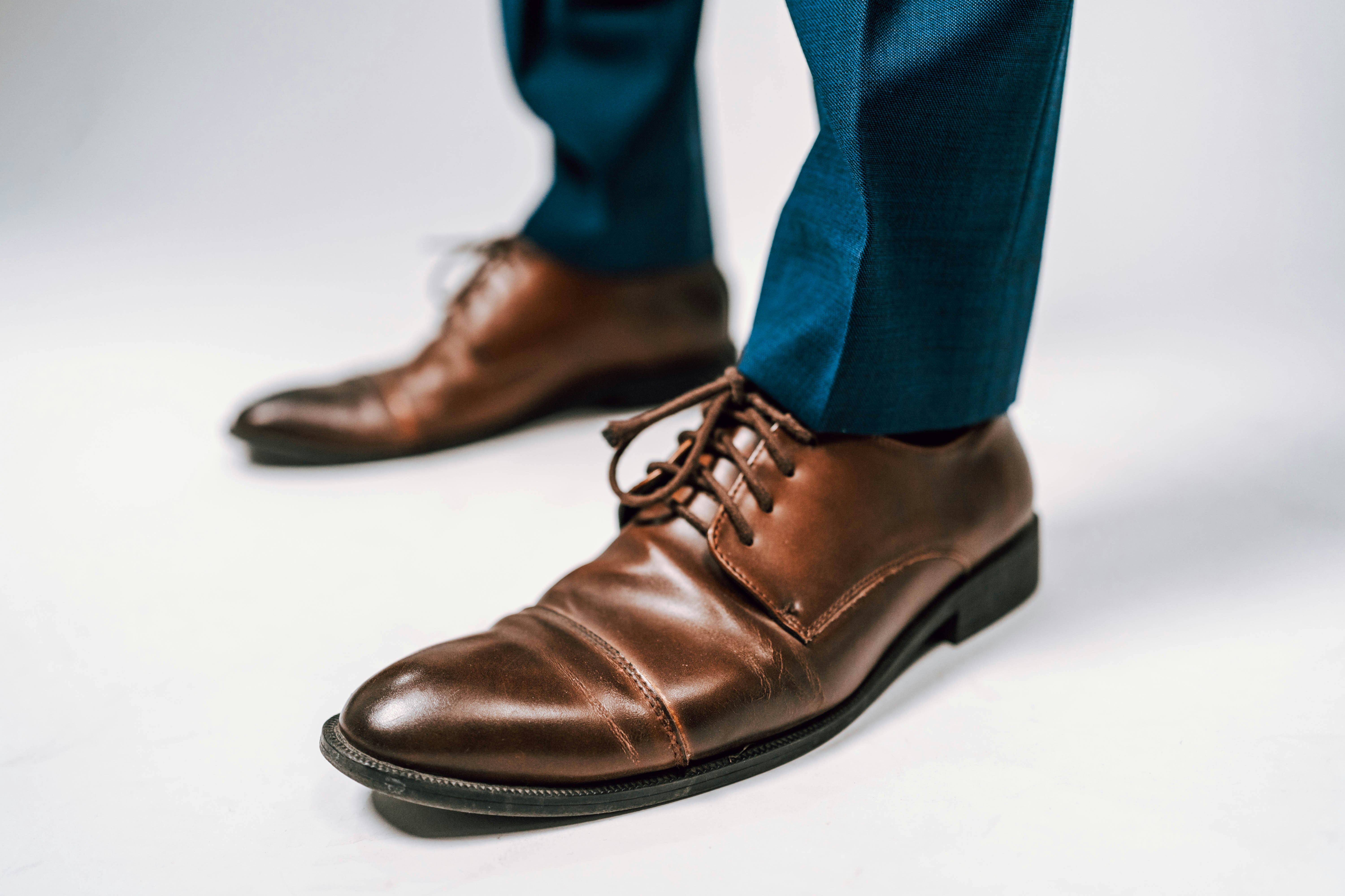 Close-up of polished brown leather shoes paired with tailored blue trousers, showcasing classic style and attention to detail.