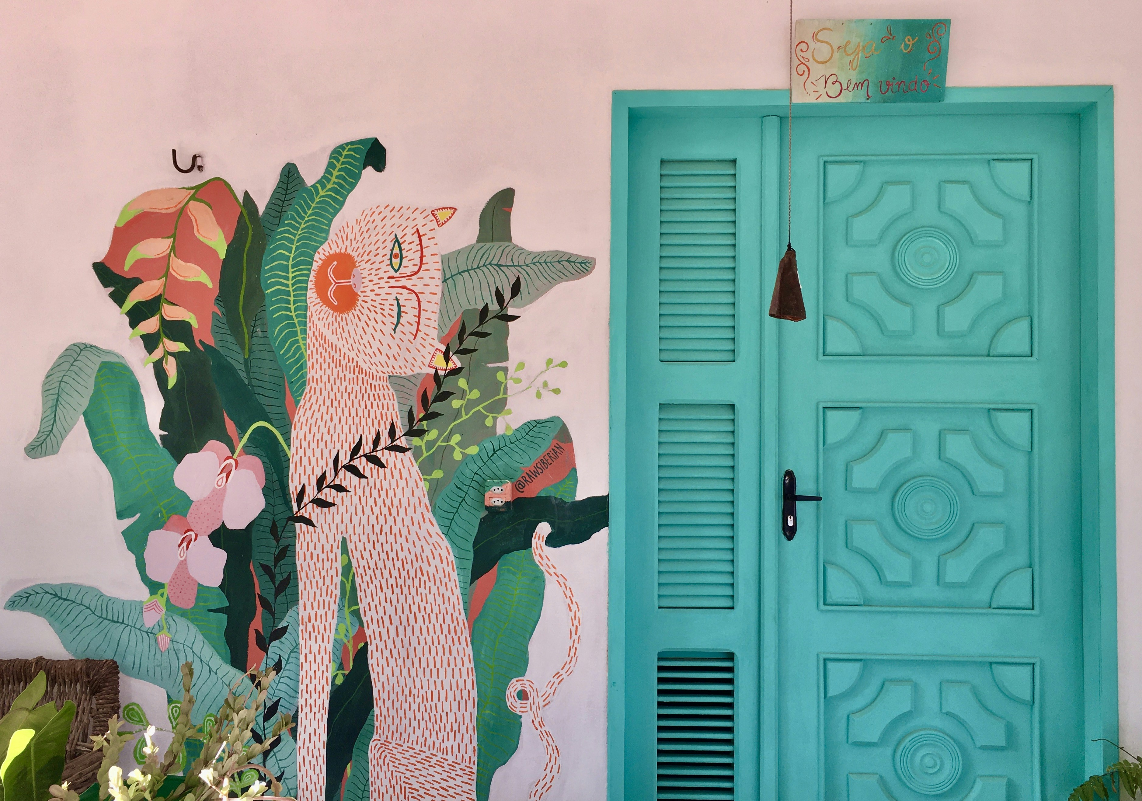 Colorful mural featuring a stylized cat entwined with tropical plants beside a vibrant turquoise door.