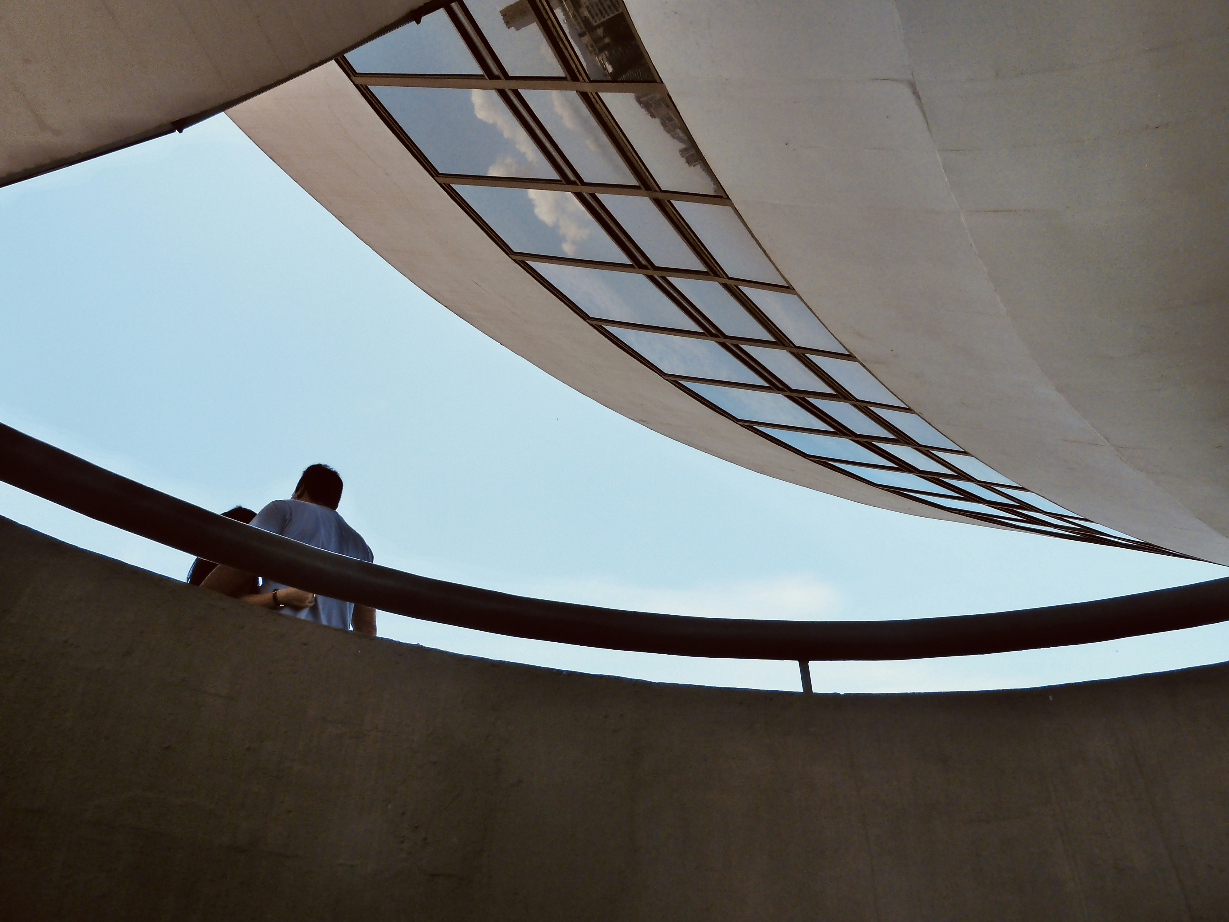 Person standing on a curved balcony with modern architectural lines against a blue sky.