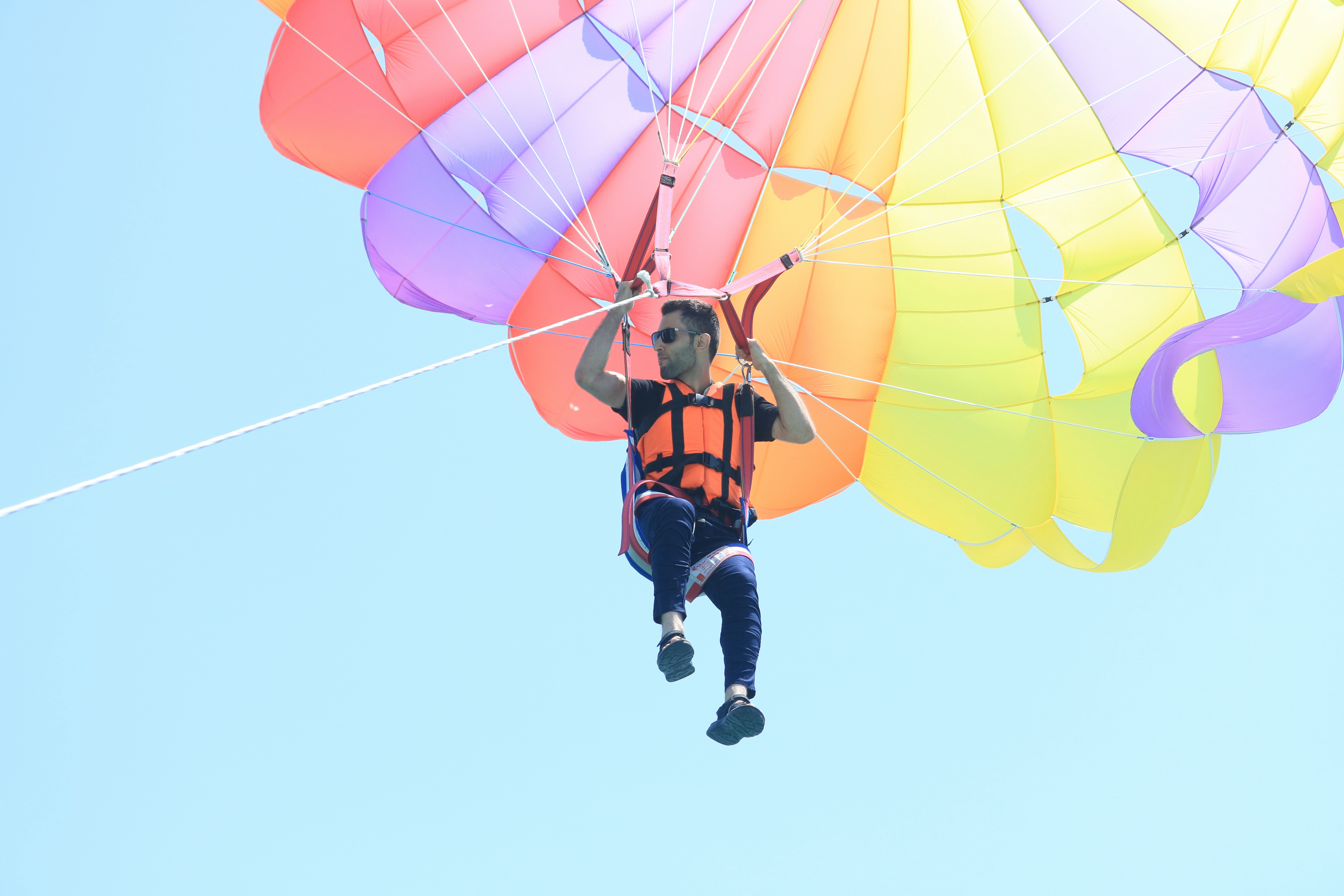 A person parasailing beneath a vibrant, multi-colored canopy against a clear blue sky.