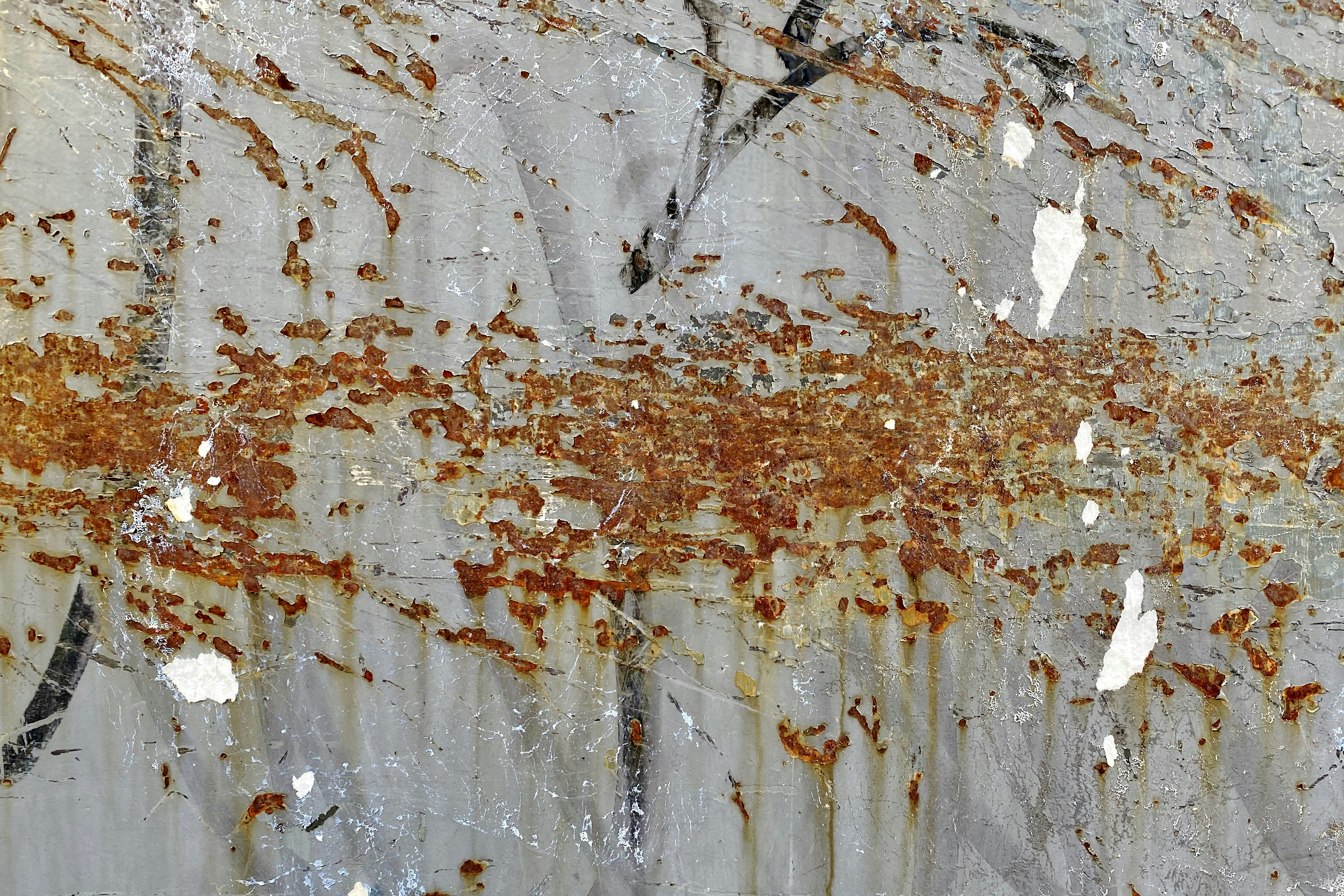 Close-up of a weathered metallic surface showcasing rust patterns and peeling paint. The interplay of textures creates a visually intriguing composition.