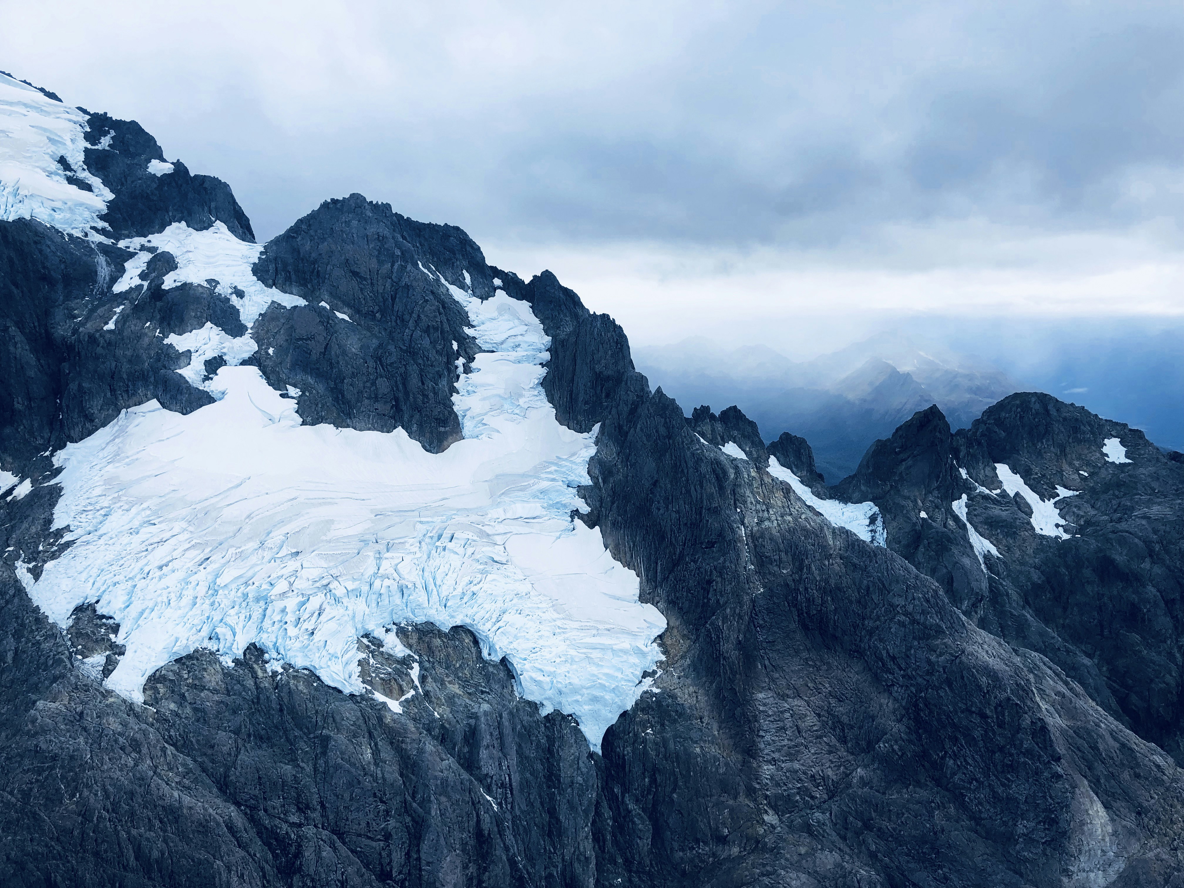 Snow-laden peaks and glaciers under a cloudy sky, revealing rugged mountain terrain.