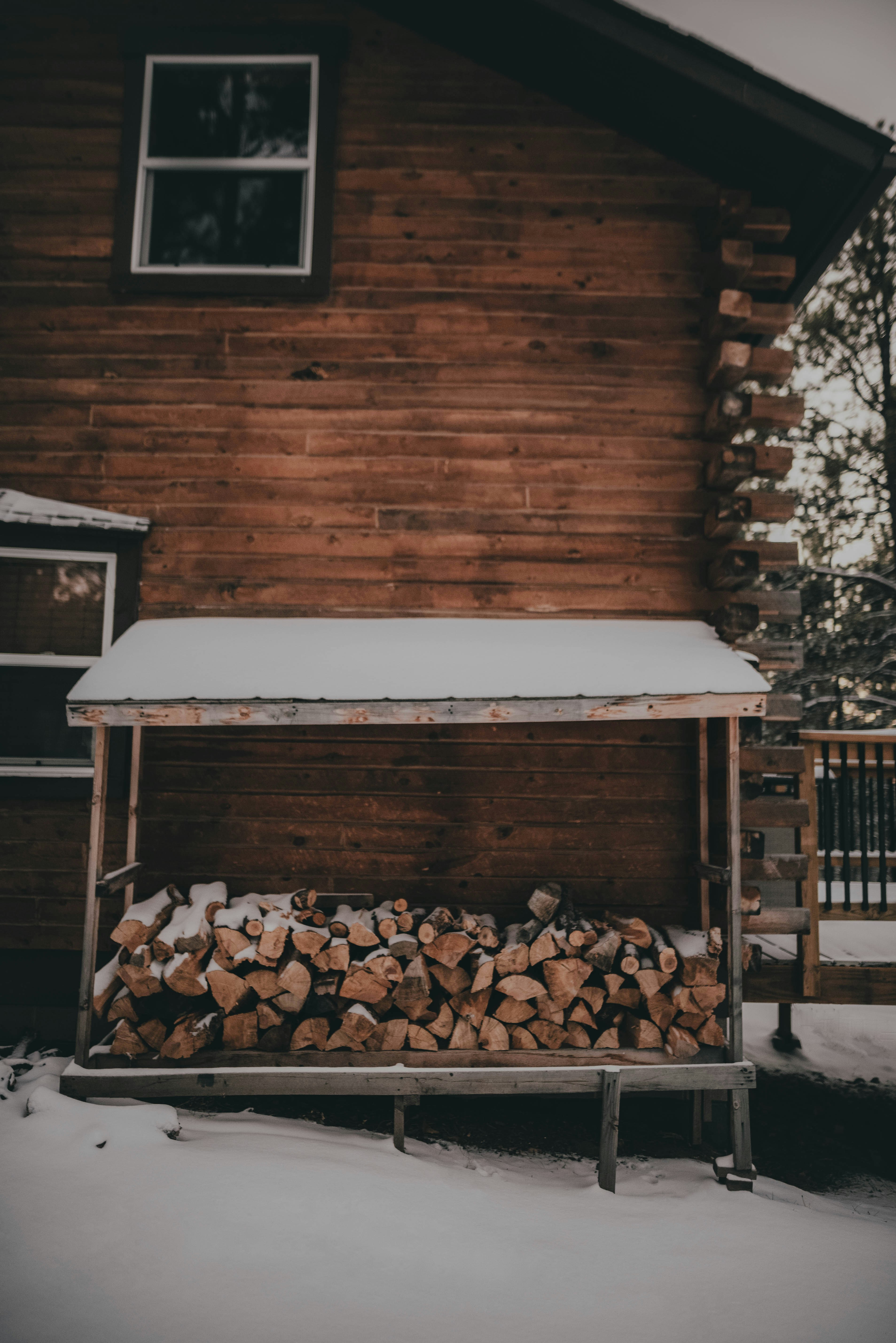 Snow-Covered Woodpile Beneath a Shelter by a Rustic Cabin