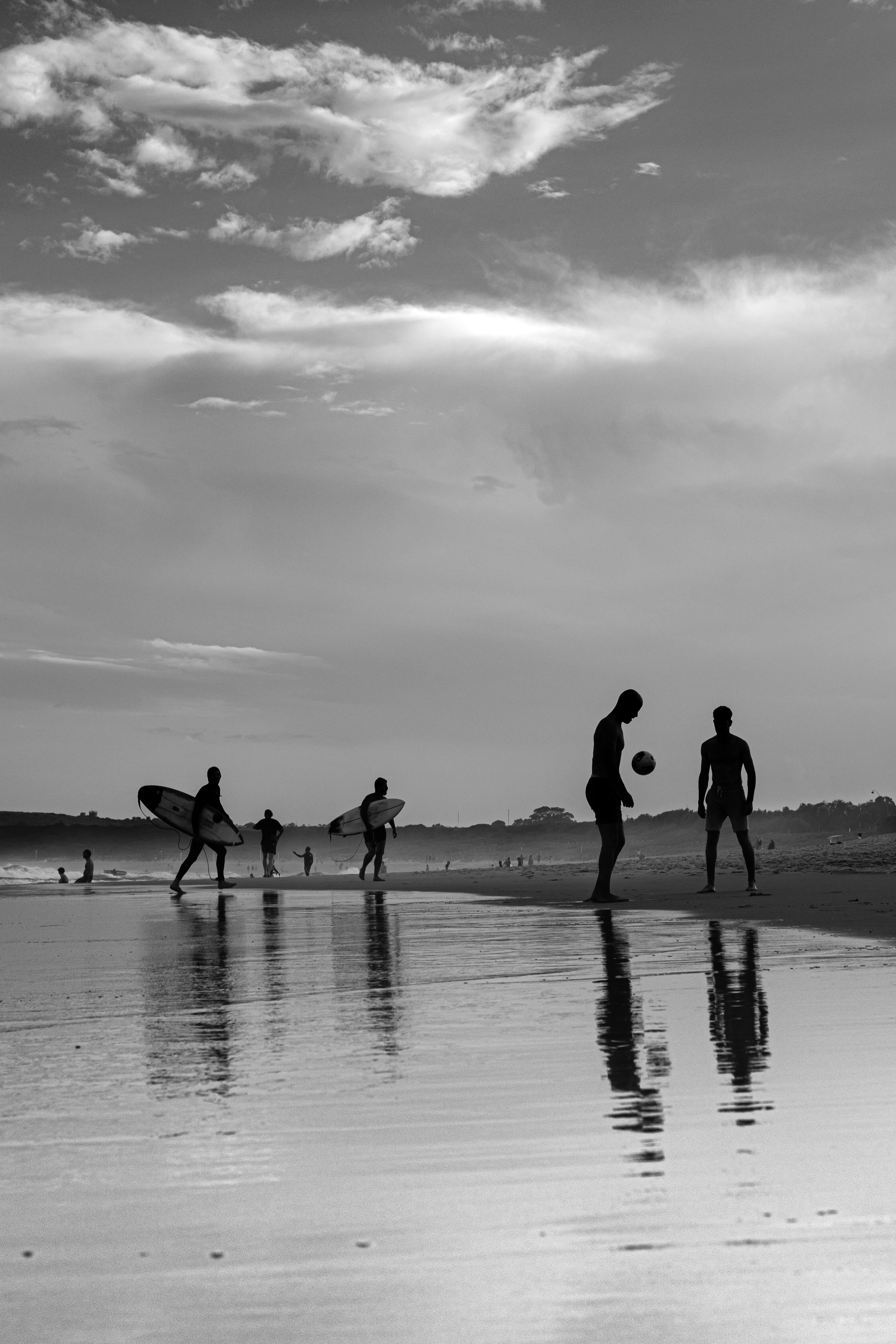 Shoreline Echoes: Silhouetted Players and Surfboards on Wet Sand