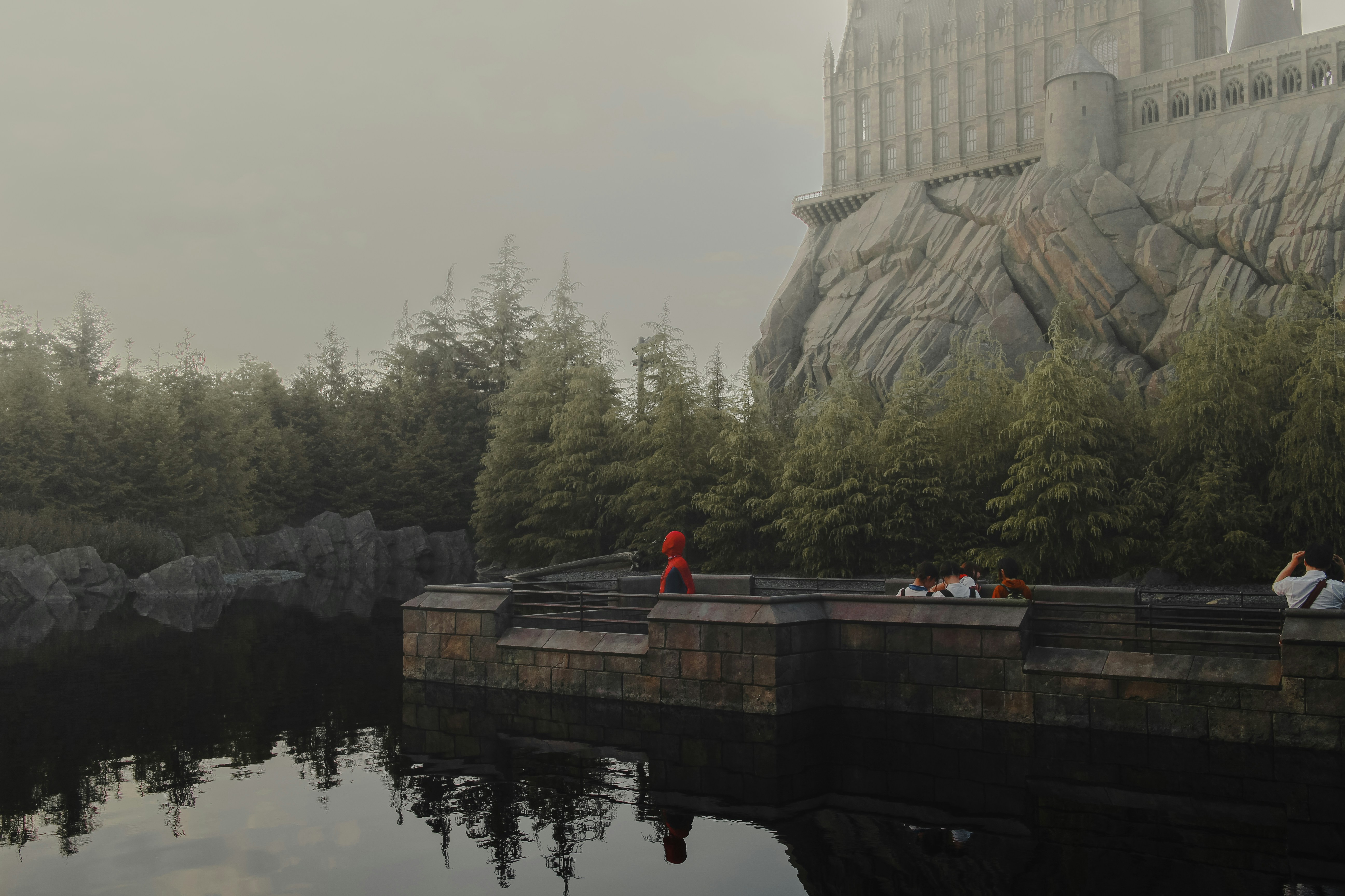 Misty overlook: a red-clad figure on stone terrace by tranquil water under looming fortress