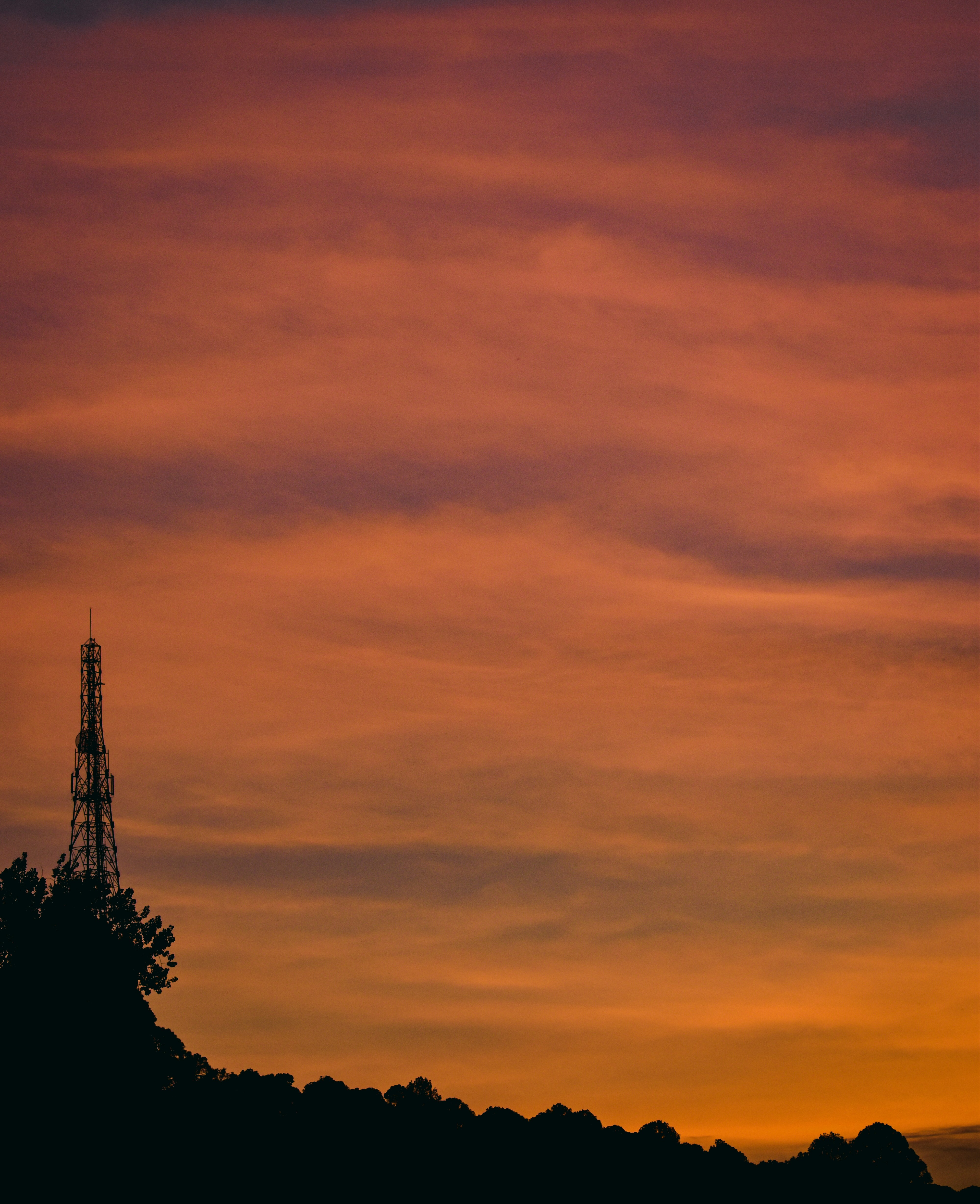Silhouette of a communication tower against a vibrant twilight sky with rich hues of orange and purple.