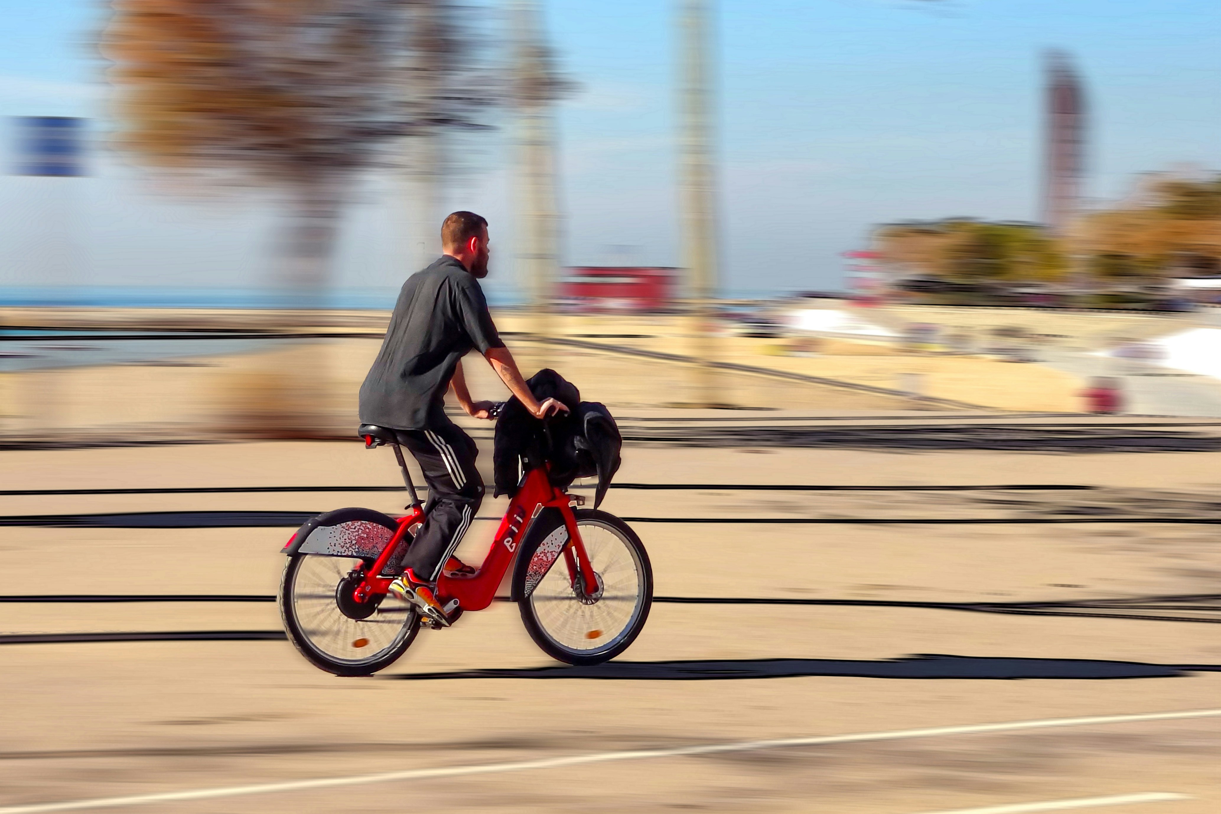Cyclist riding a red bike along a sunlit coastal path with motion blur capturing movement.