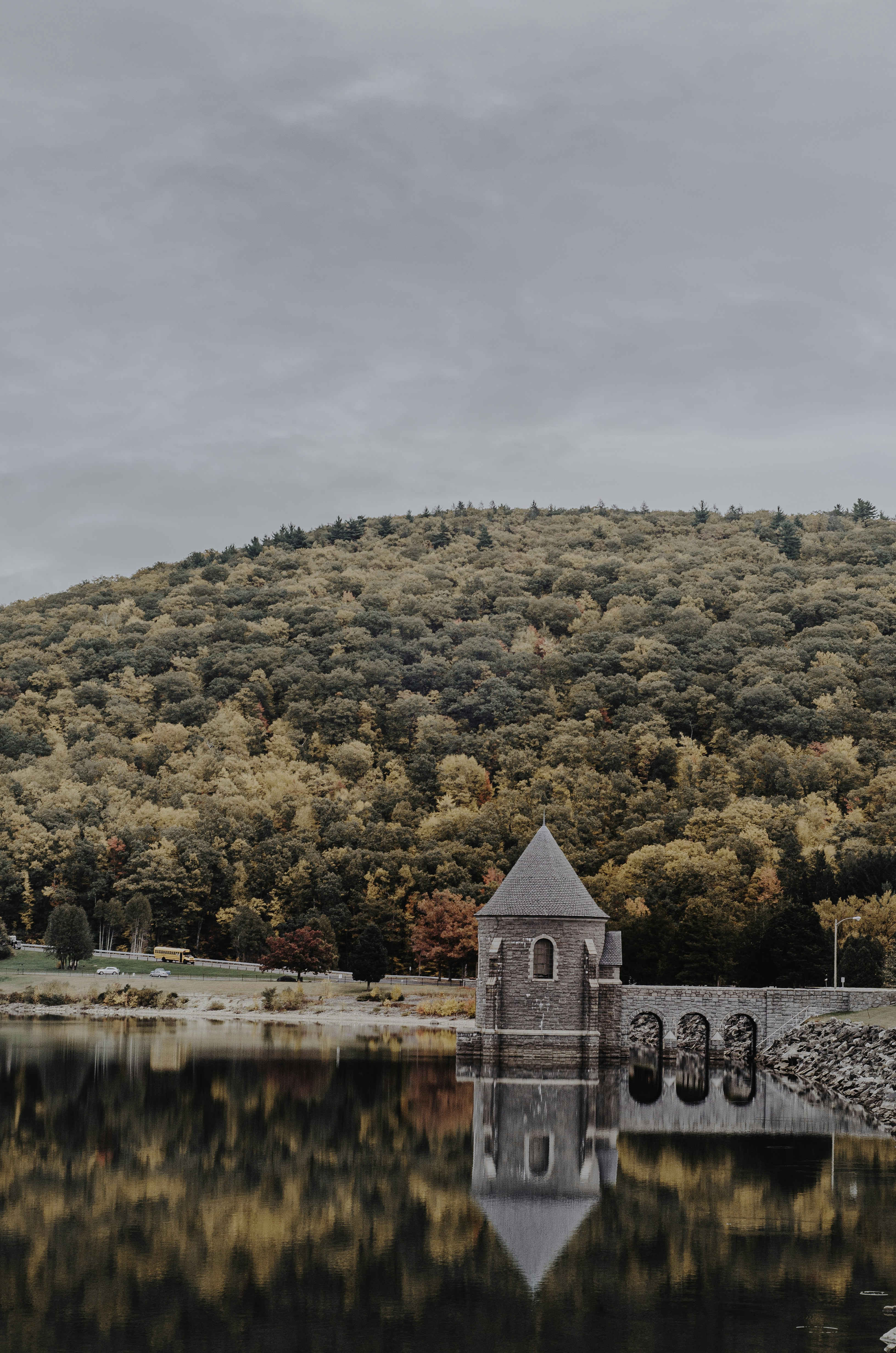 Historic stone structure by a calm lake, surrounded by autumn foliage reflecting on the water's surface.