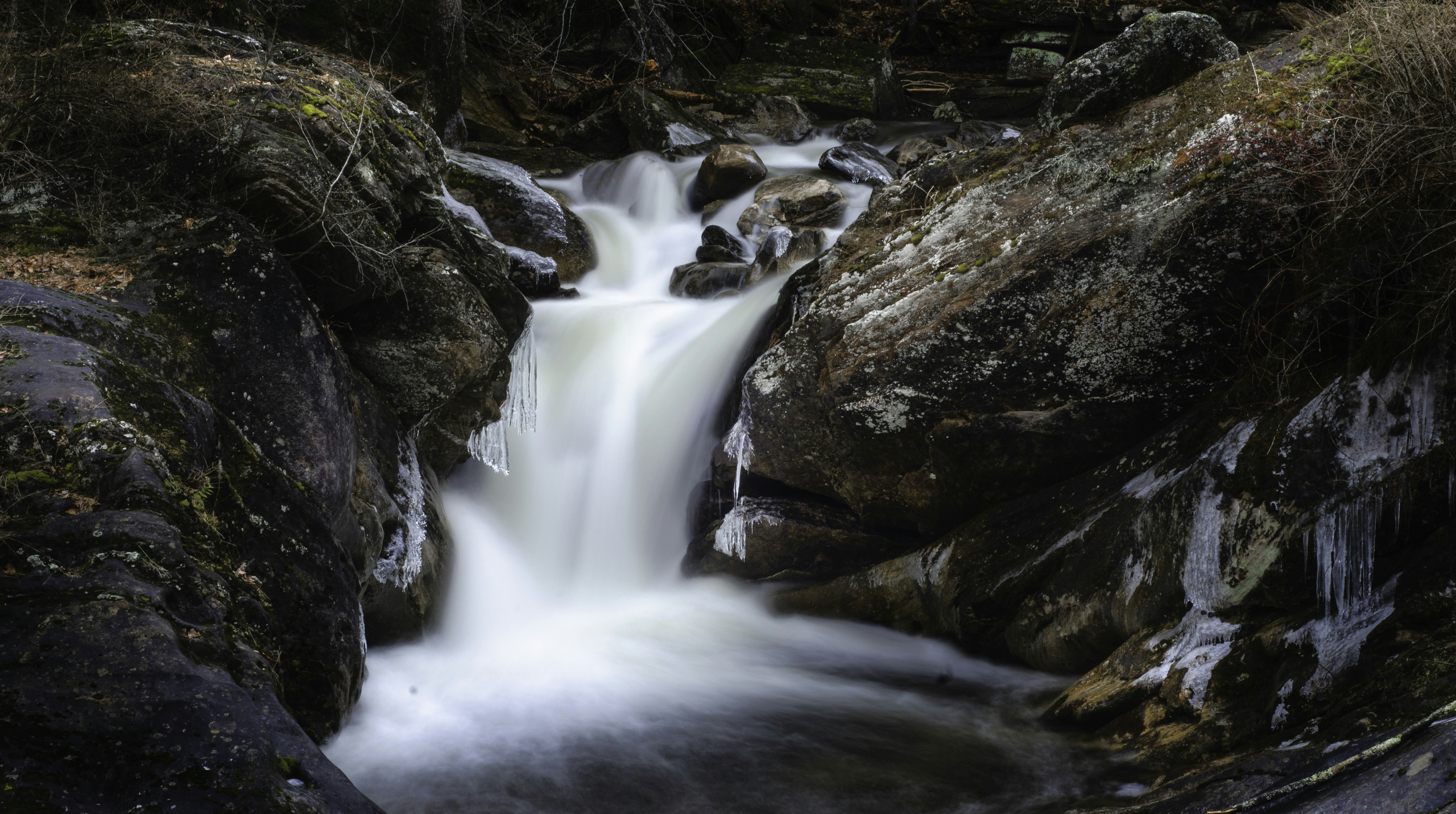 Smooth waterfall flows between moss-covered rocks, creating an ethereal scene in a forest setting.
