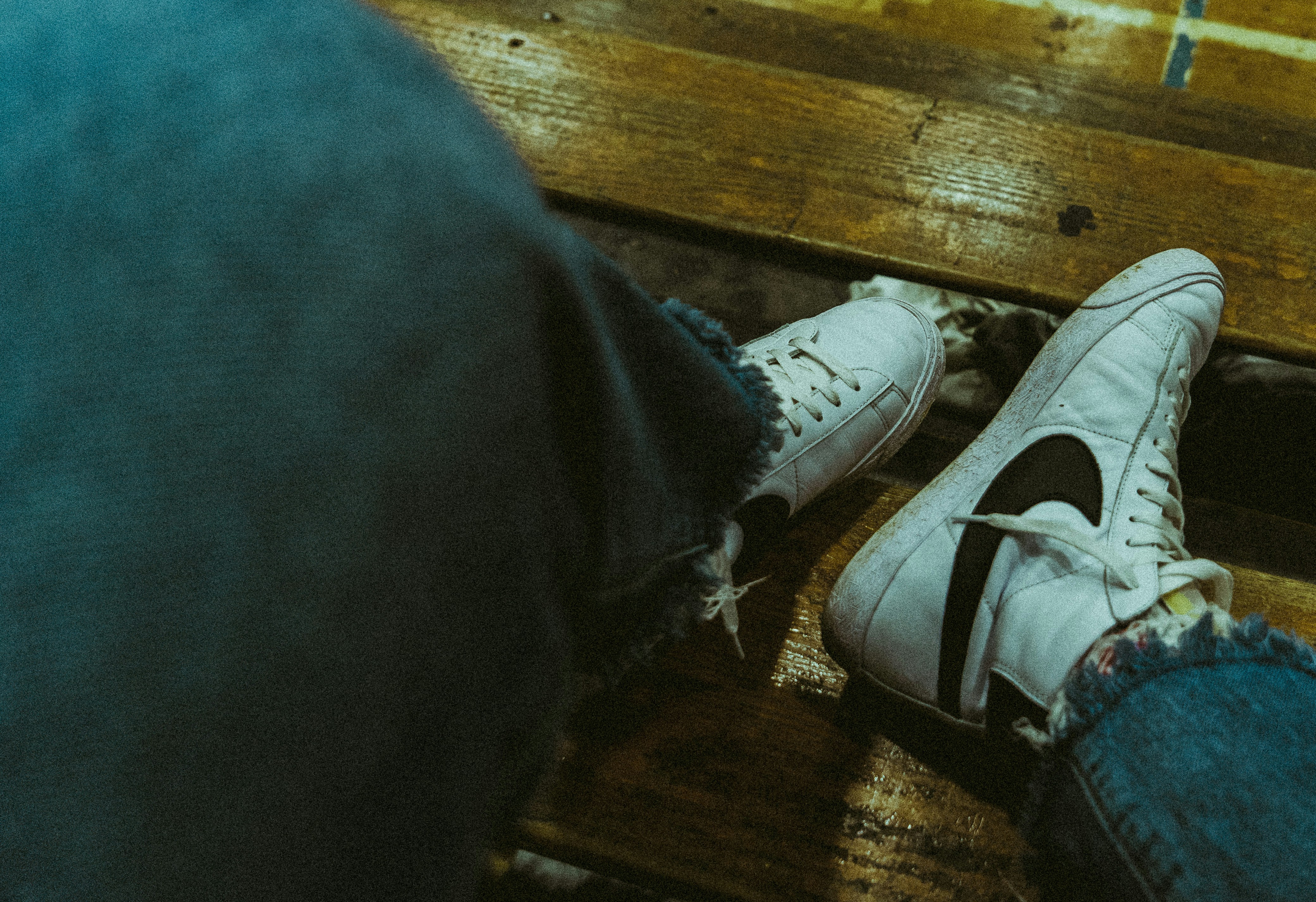 White Nike sneakers resting on wooden bleachers, showcasing a casual urban vibe. The worn denim adds a touch of everyday life.
