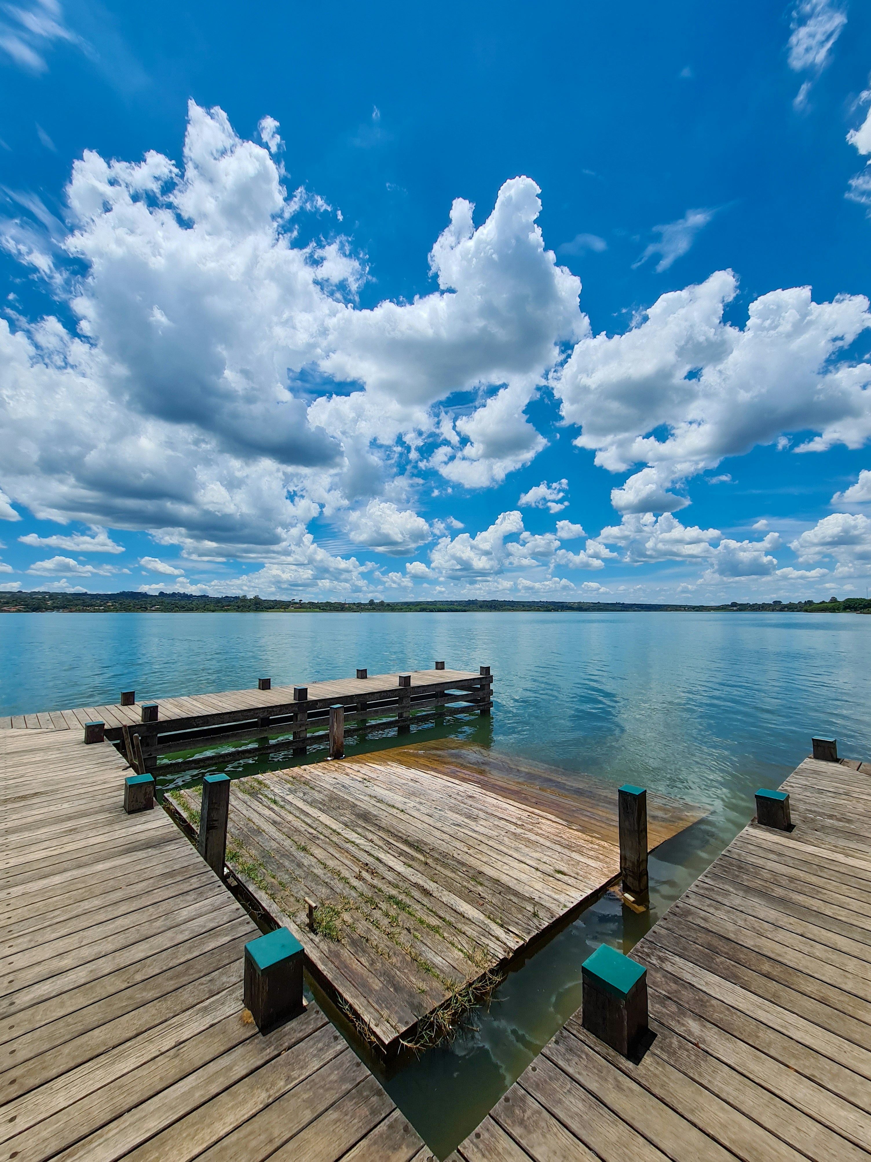 Wooden docks extend into a serene lake under a vibrant sky filled with fluffy clouds. The calm water reflects the surrounding beauty.