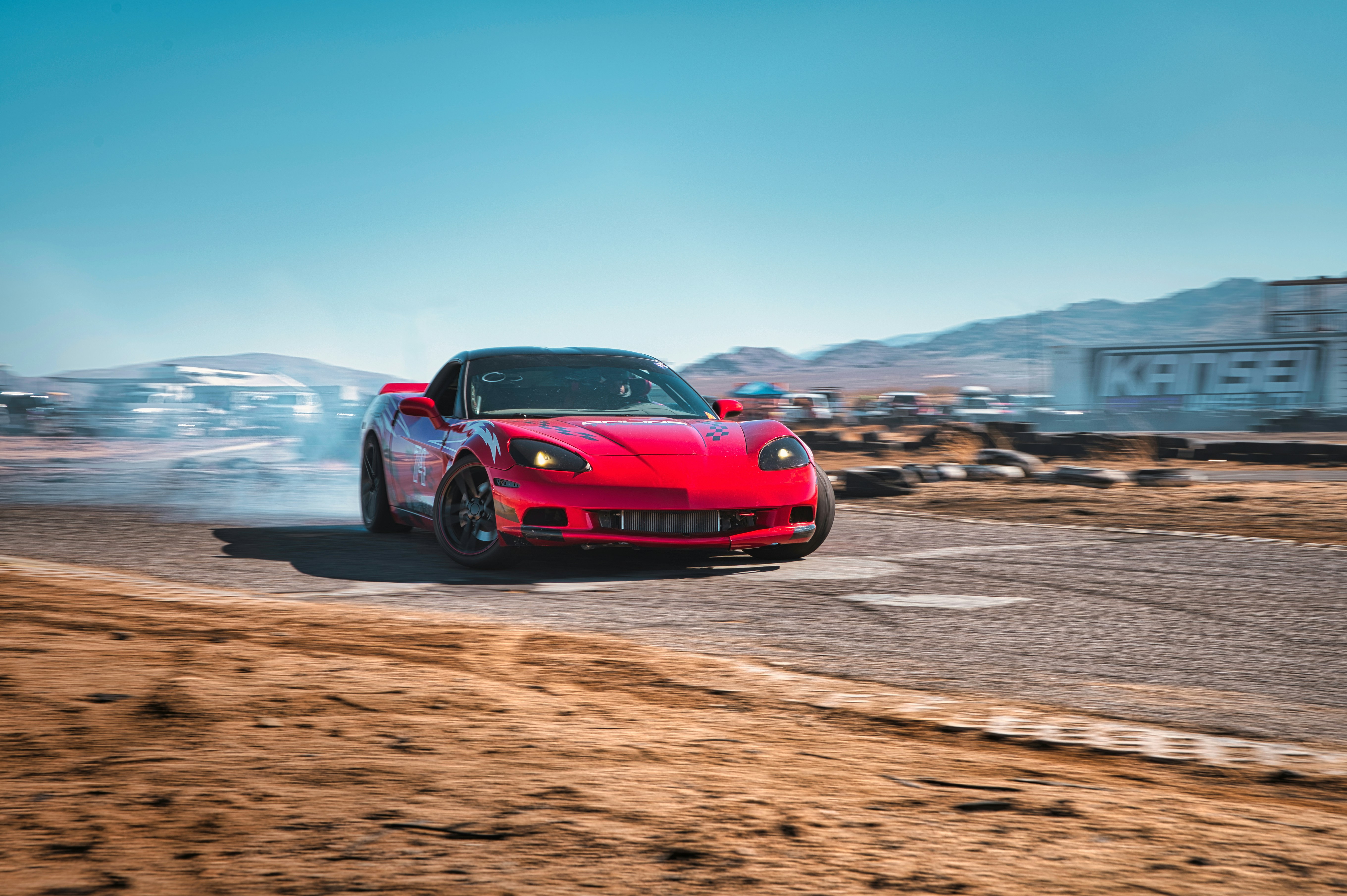Red sports car drifting on a sunlit race track with mountains in the background.