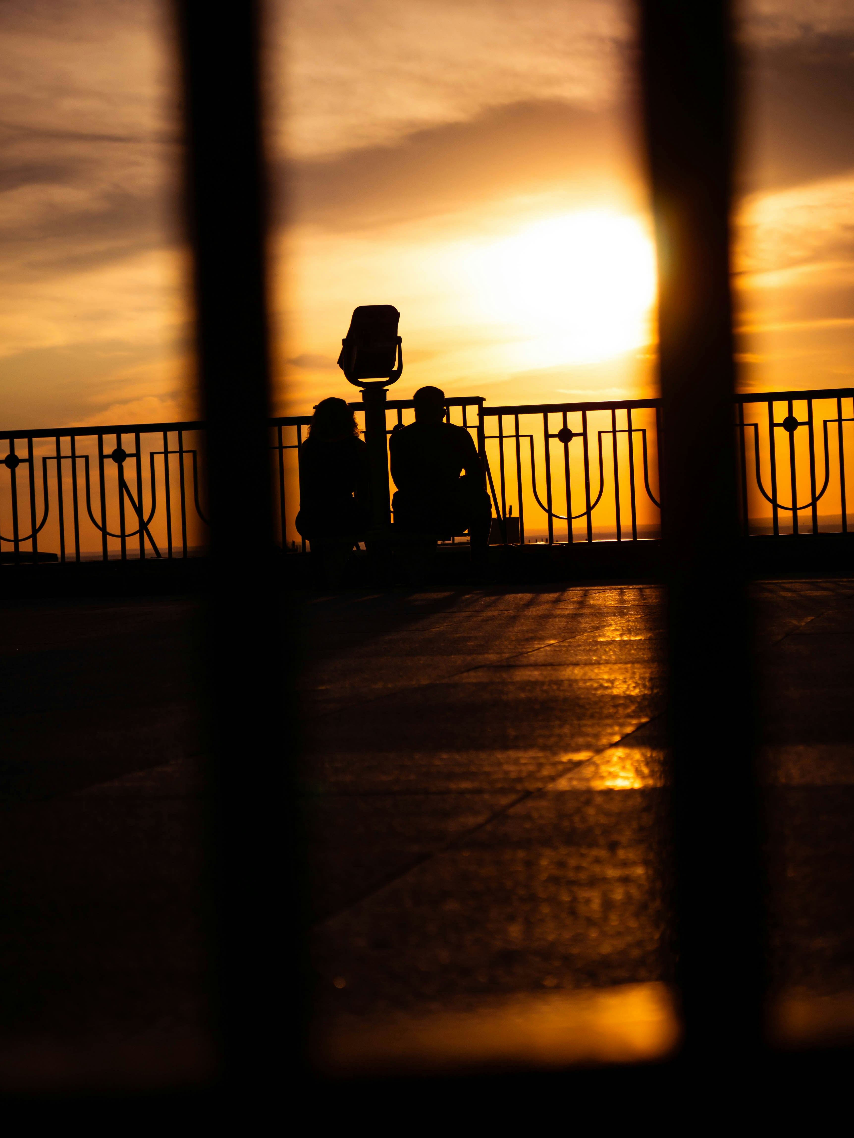 Dusk Silhouettes by the Rail: Two Figures and a Viewing Telescope at Sunset