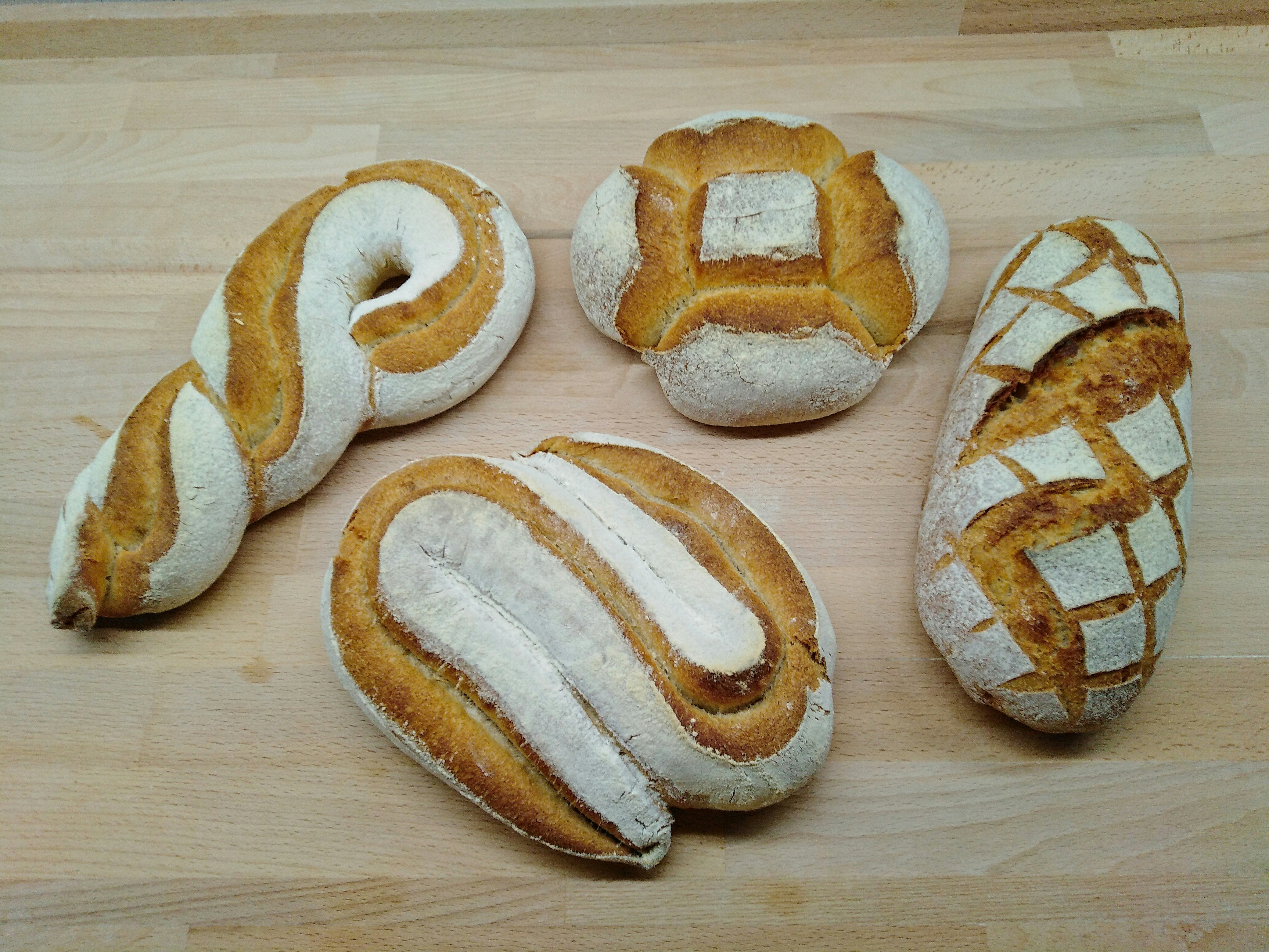 Four uniquely shaped artisan bread loaves arranged on a wooden surface, showcasing intricate designs and textures.