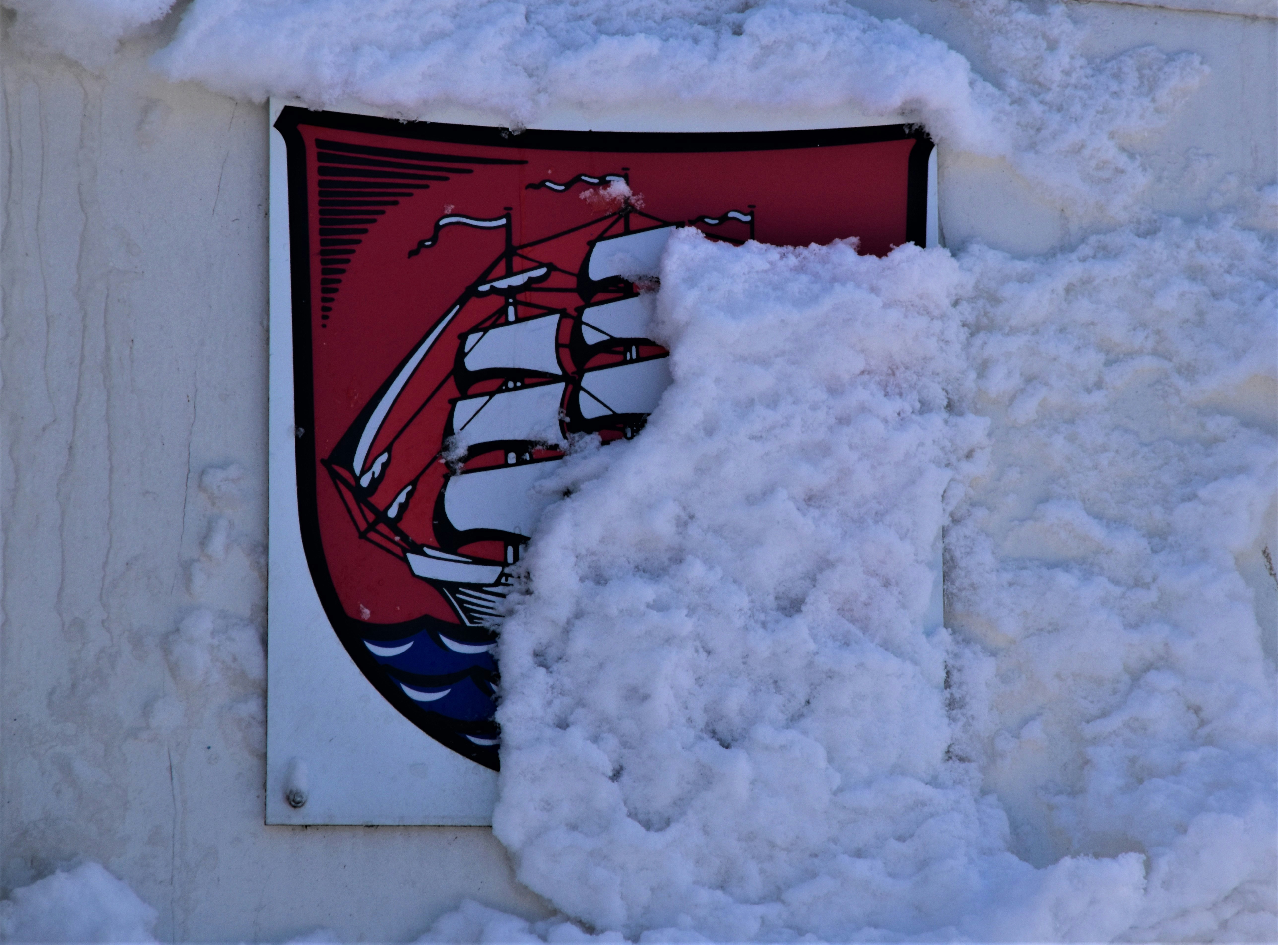A weathered emblem featuring a ship partially obscured by snow, symbolizing resilience in harsh winter conditions.