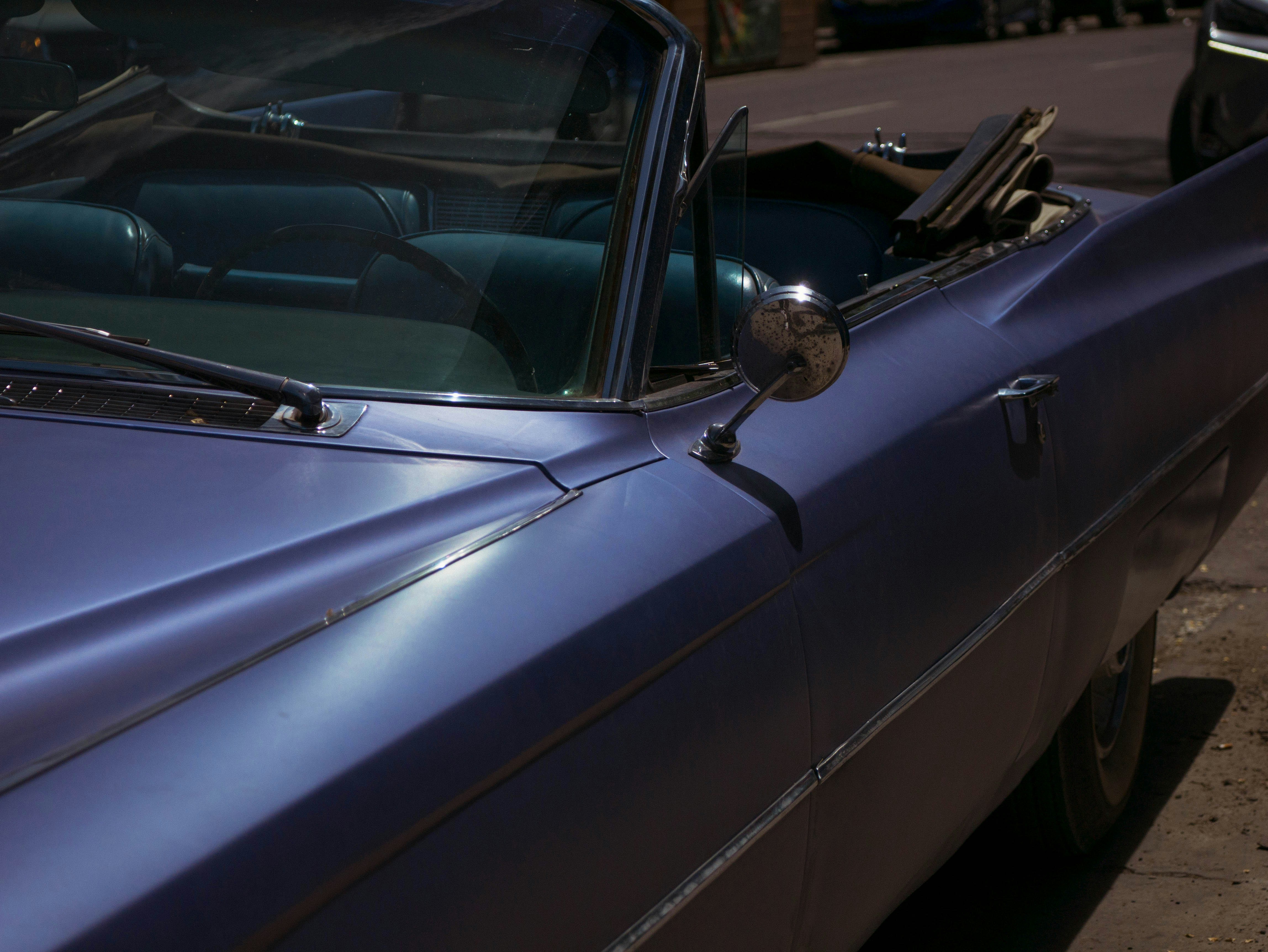 Close-up of a vintage convertible with a sleek purple exterior and turquoise interior, showcasing its elegant lines and chrome details.