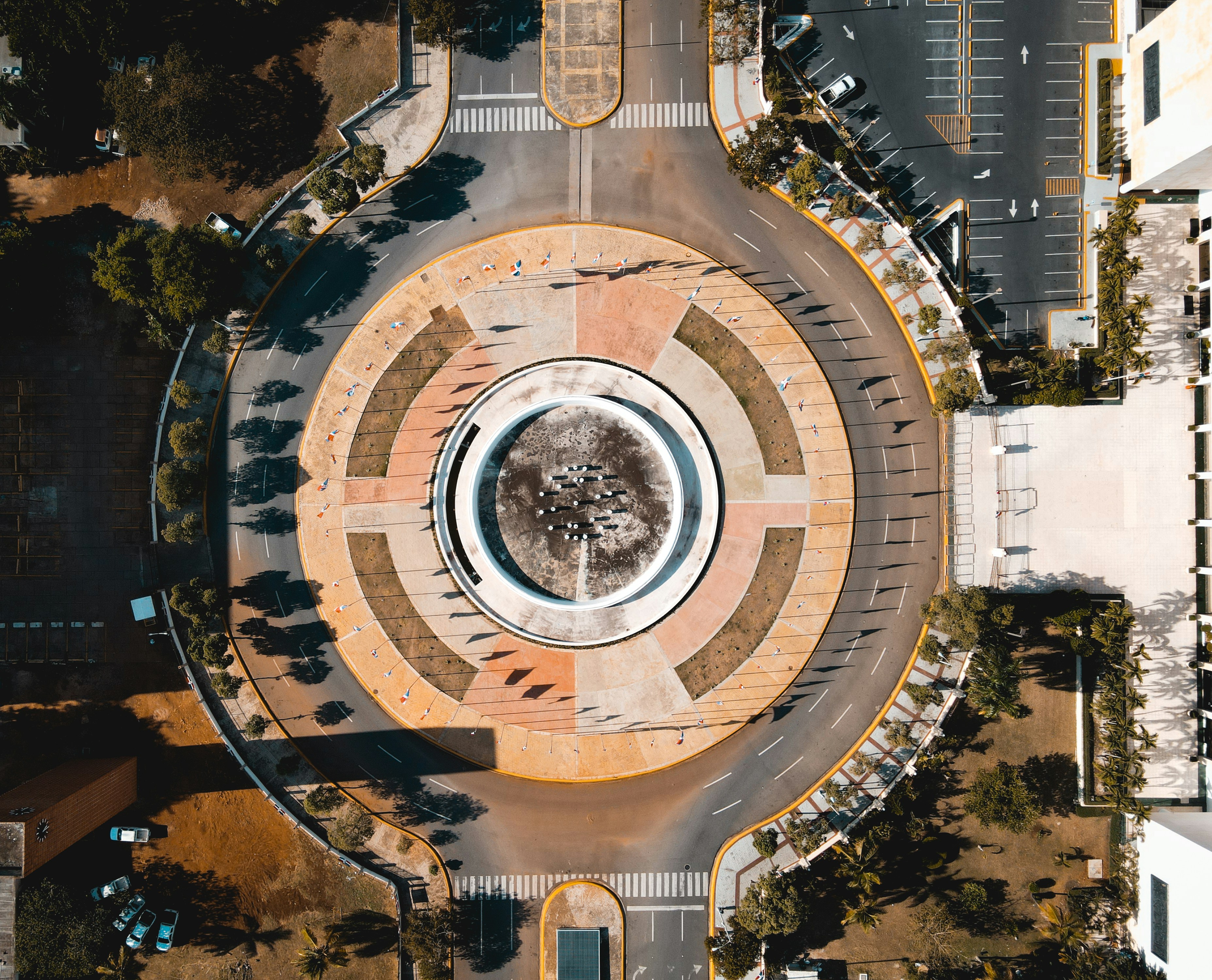 Aerial view of a circular roundabout with a central tree, surrounded by roads and parked cars.