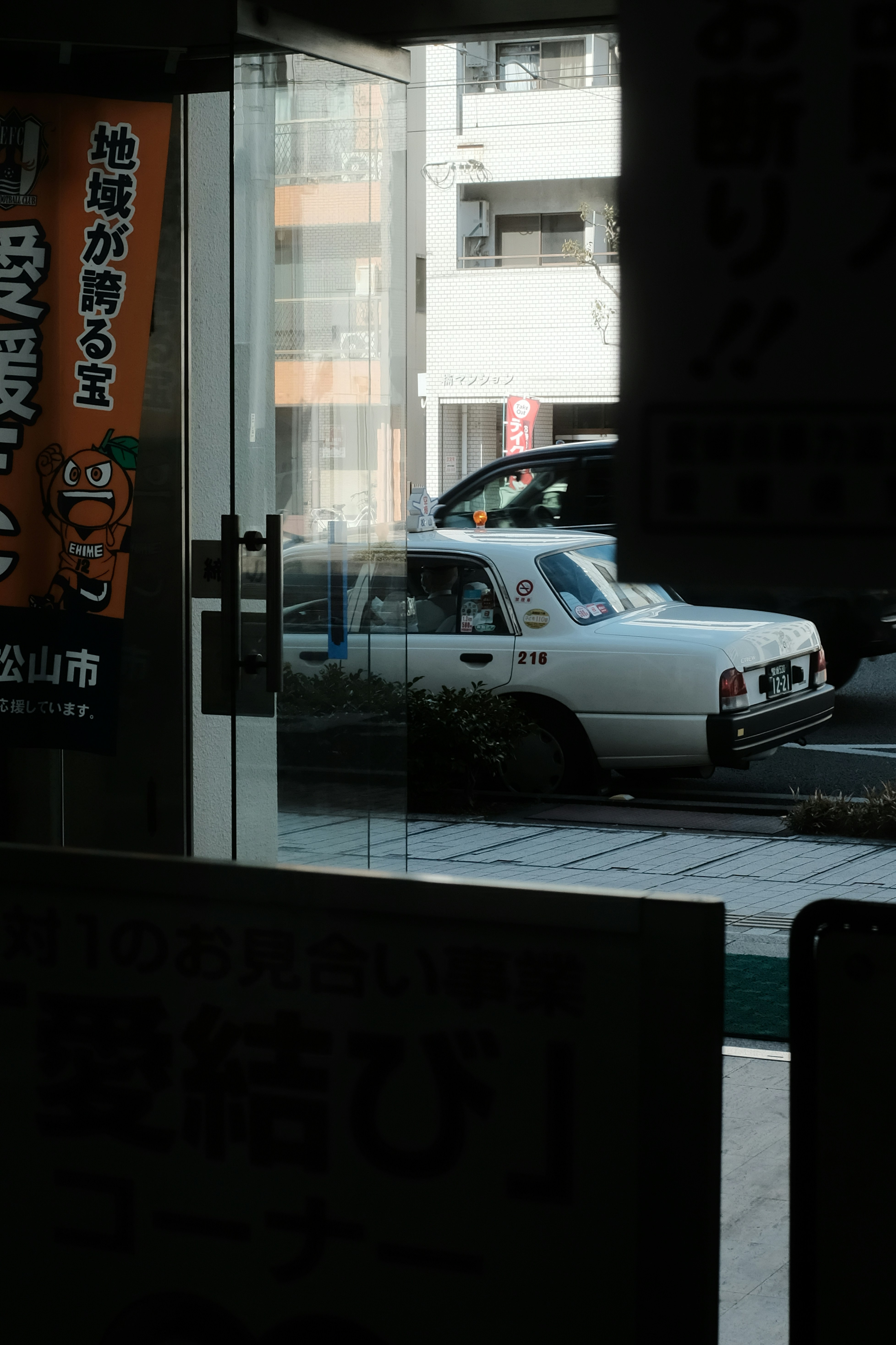 A vintage taxi parked on a city street, framed by storefront reflections and colorful signage. The scene captures the essence of urban life.