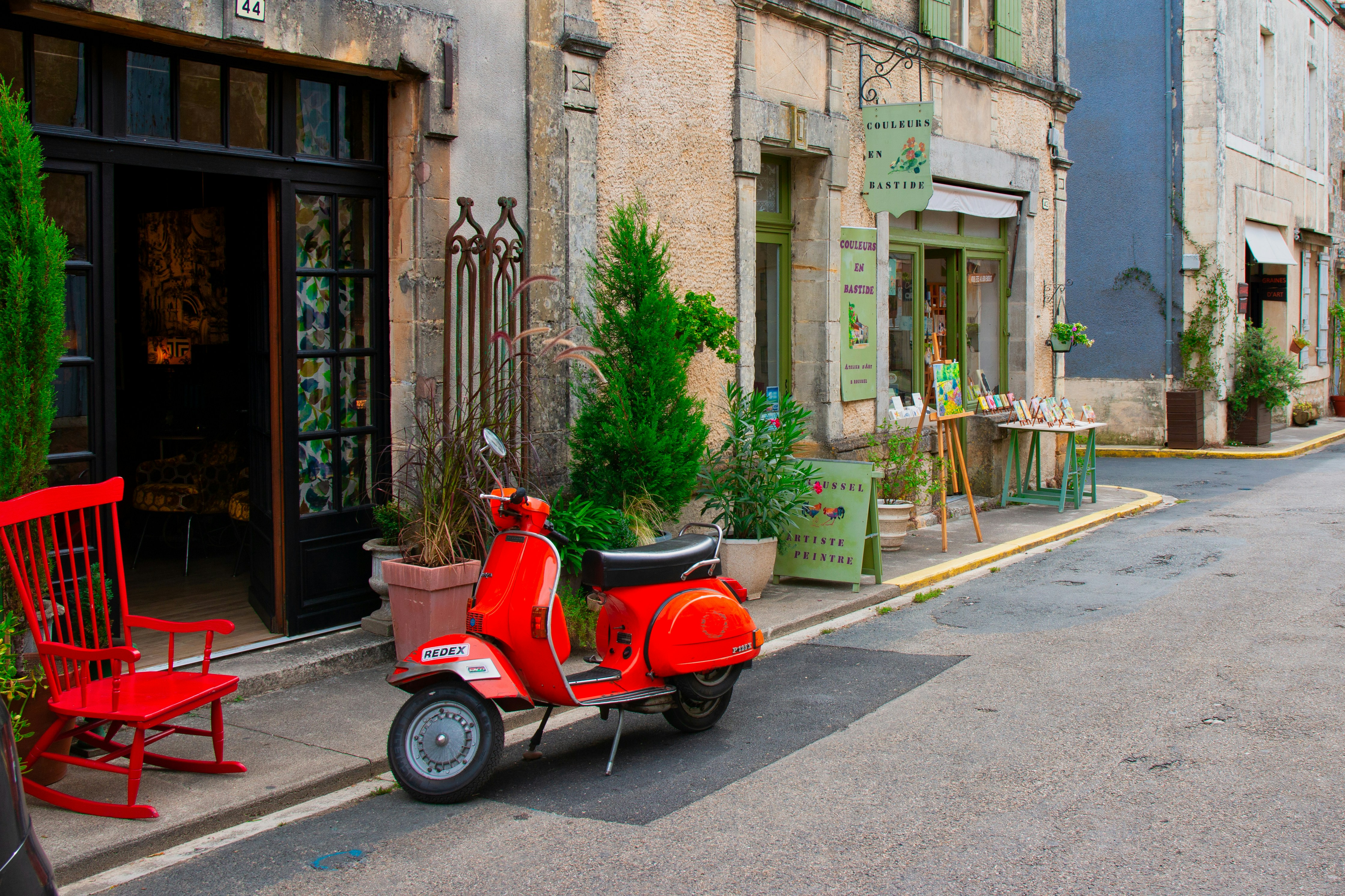 Red Vespa Pausing by a Café-Lined Street