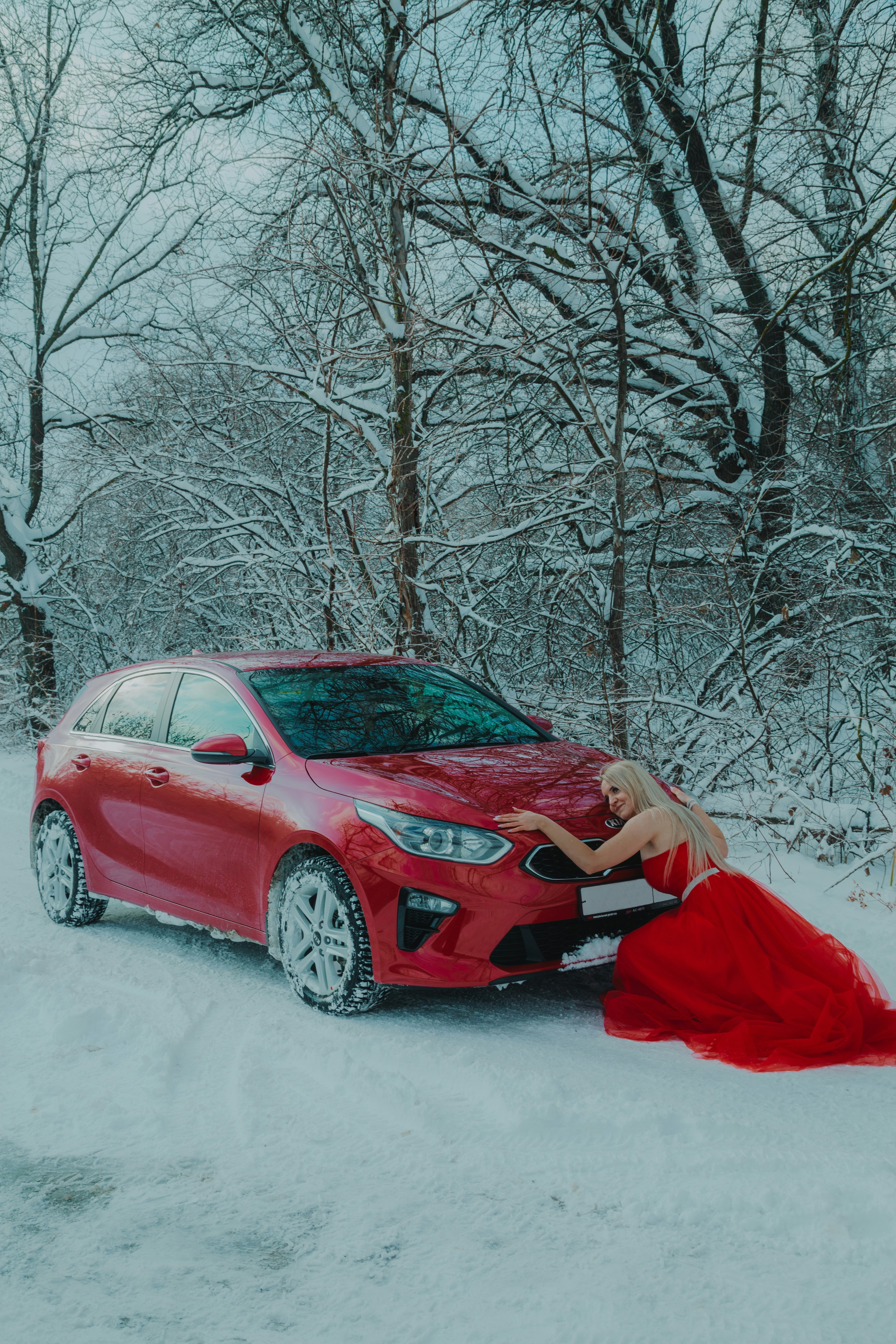 woman in red jacket and red pants sitting on snow covered ground near red sedan
