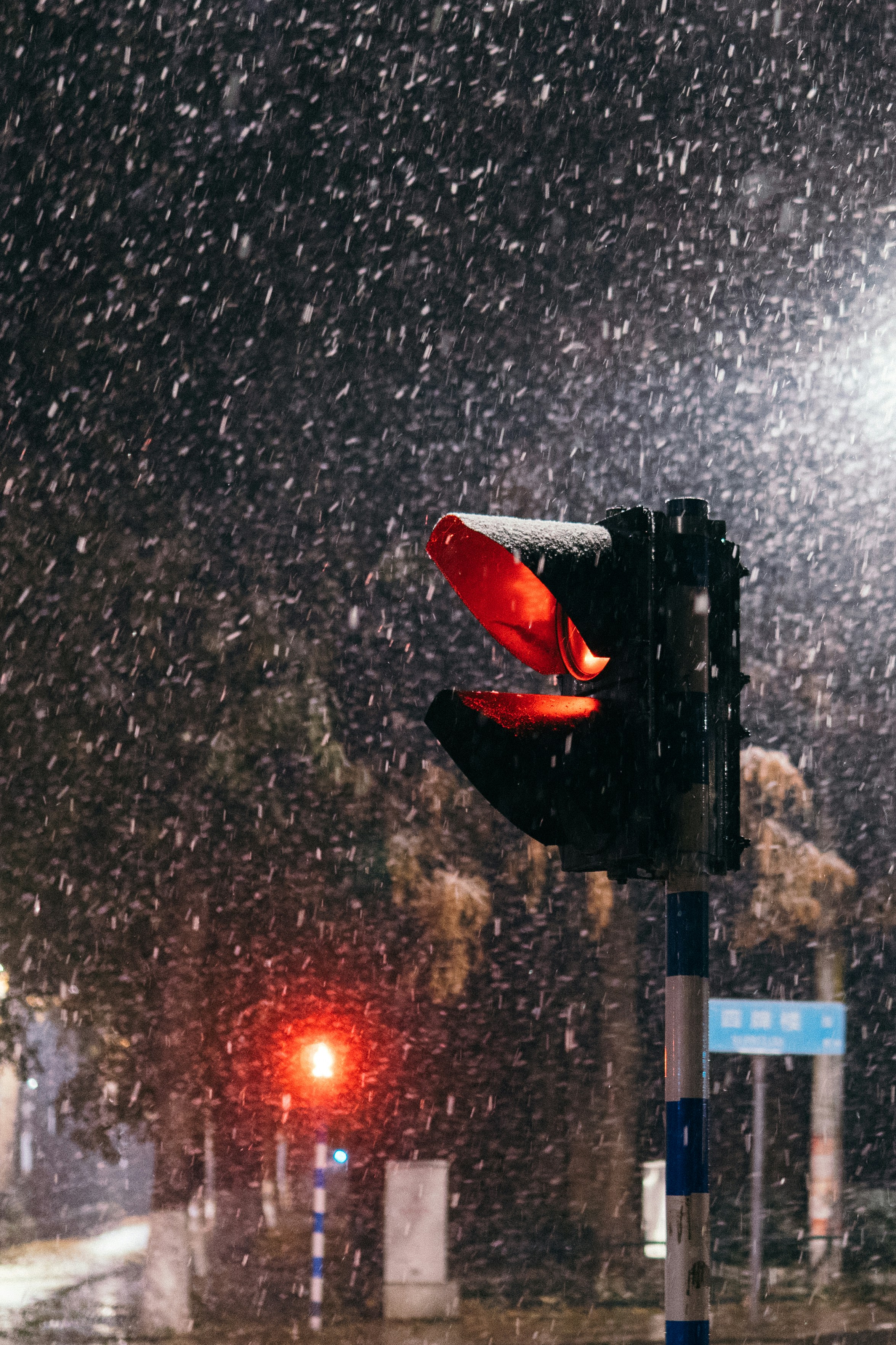 Red traffic light illuminated against a backdrop of heavy snowfall at night.