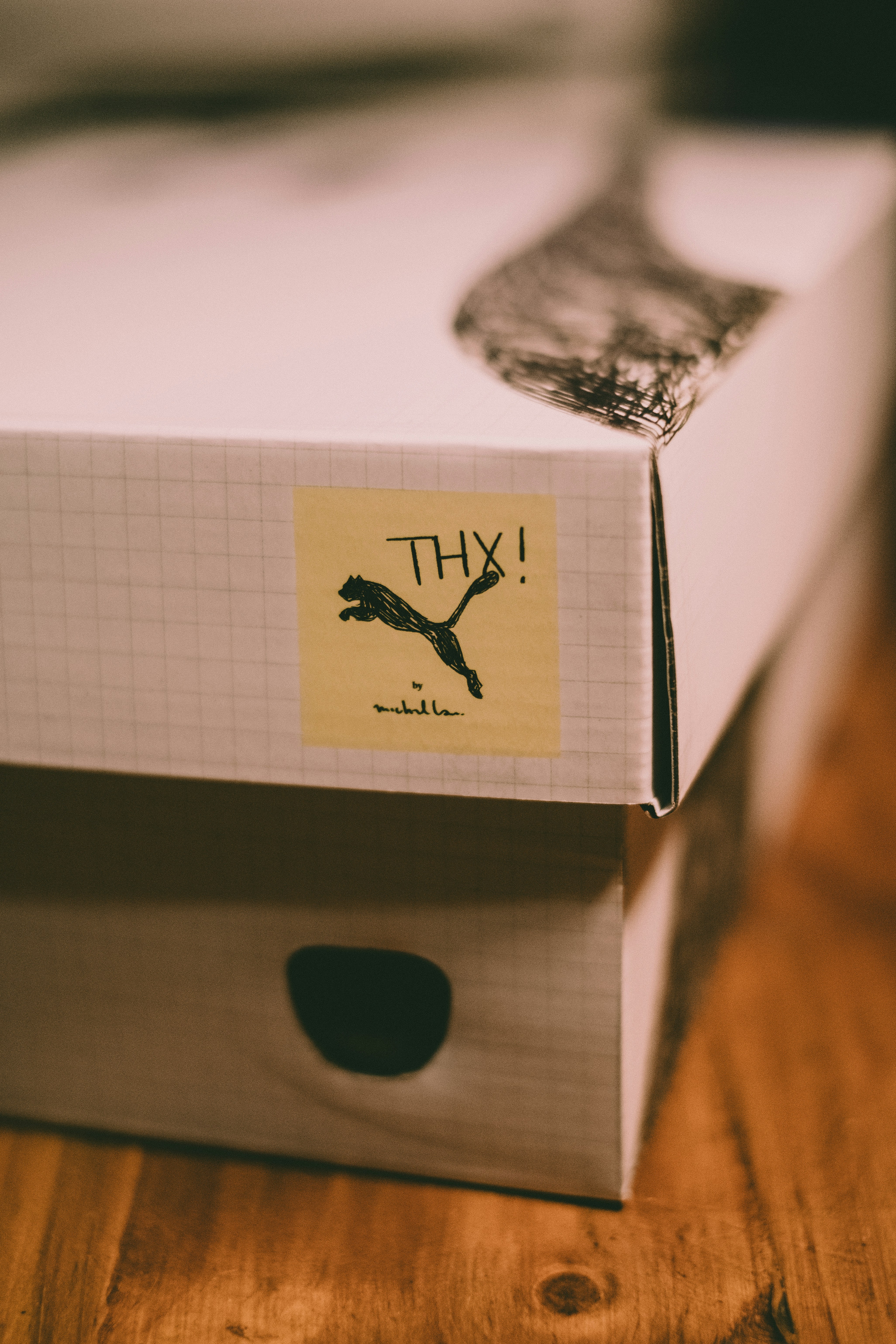 A creatively designed box featuring a playful 'THX!' note with a stylized illustration of a leaping figure. The box is set against a warm wooden background.