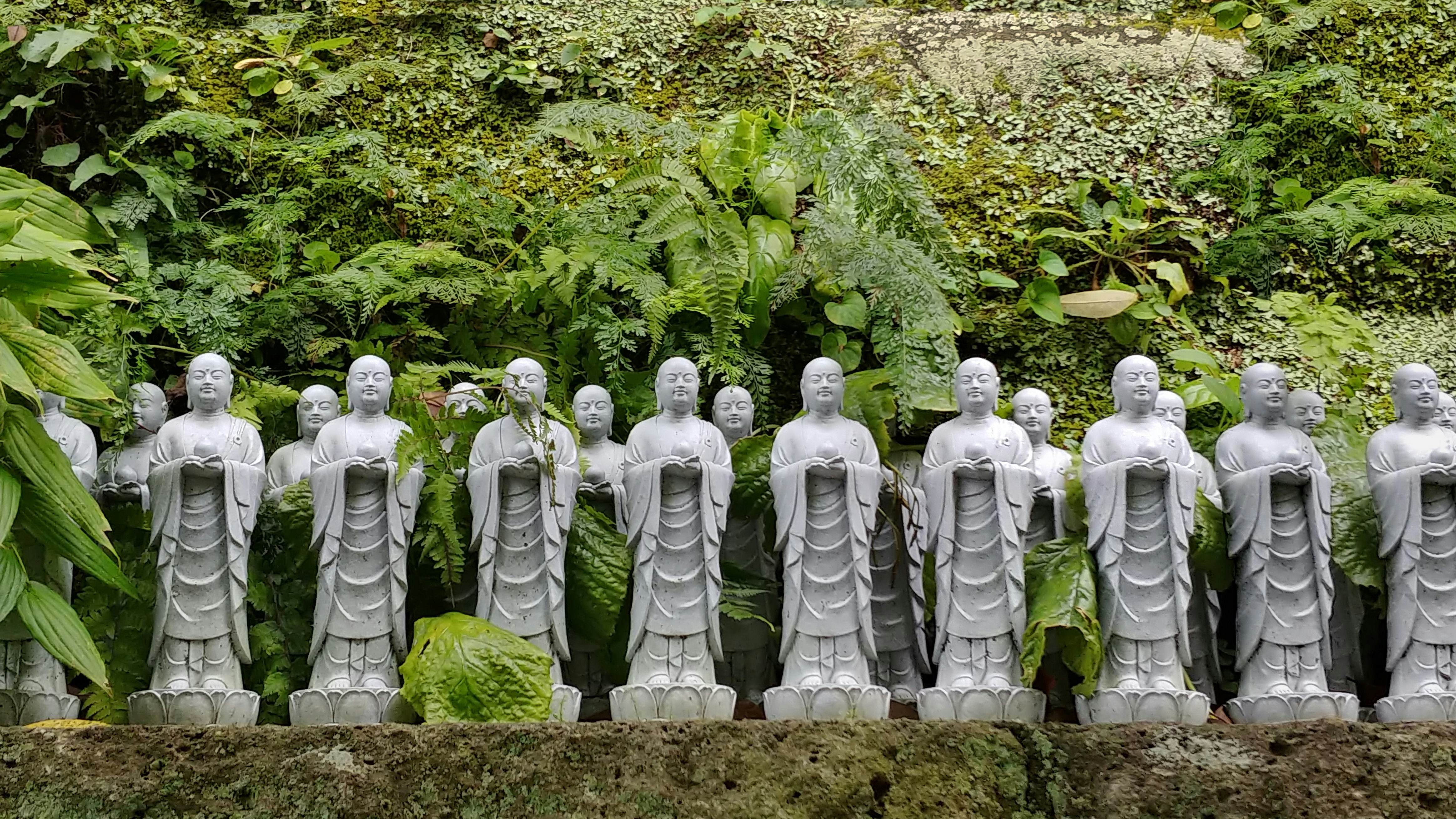 A row of serene stone statues stands amidst lush greenery, symbolizing tranquility and reflection.