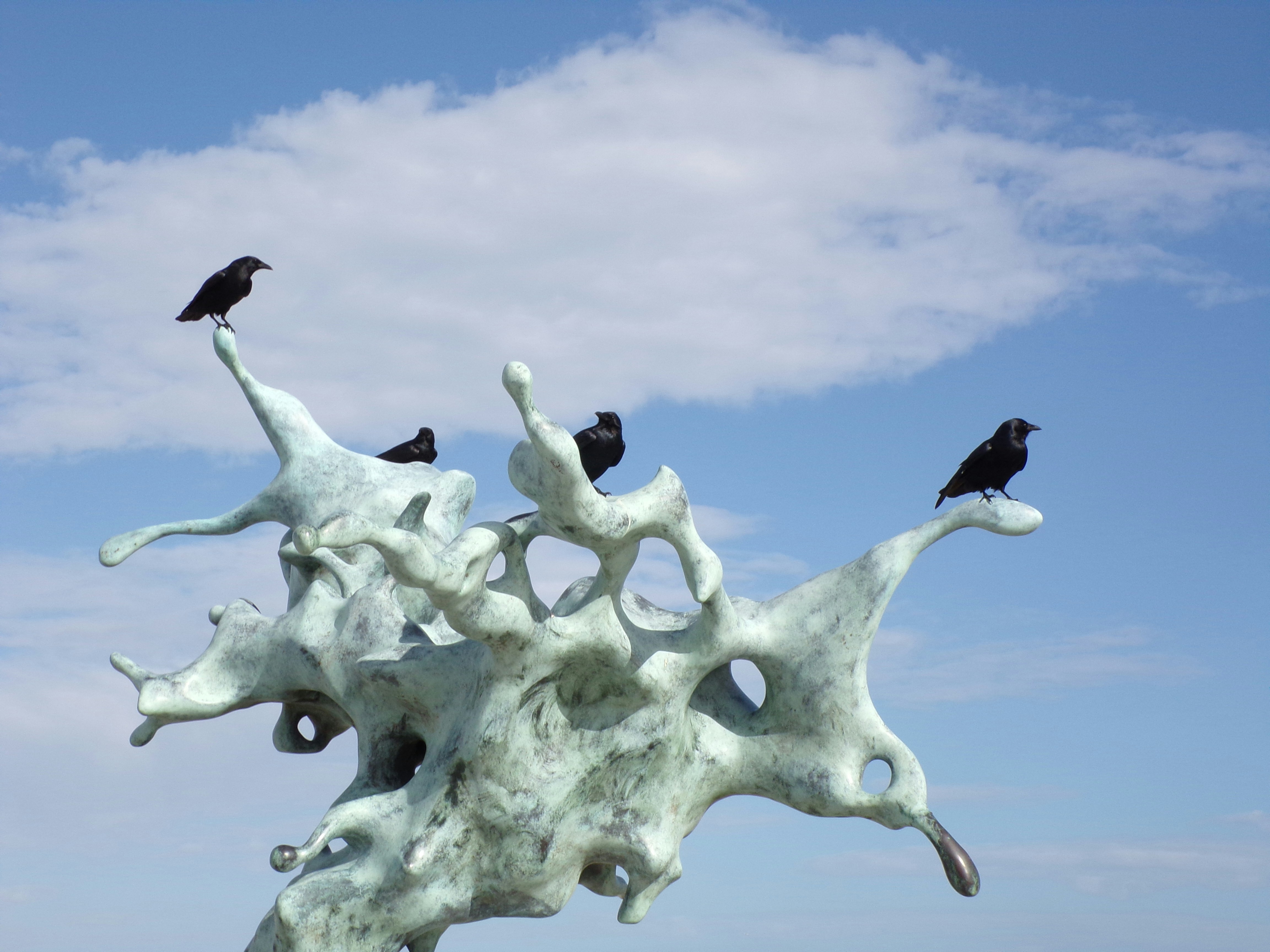 Abstract sculpture with birds perched on its organic forms against a clear blue sky.