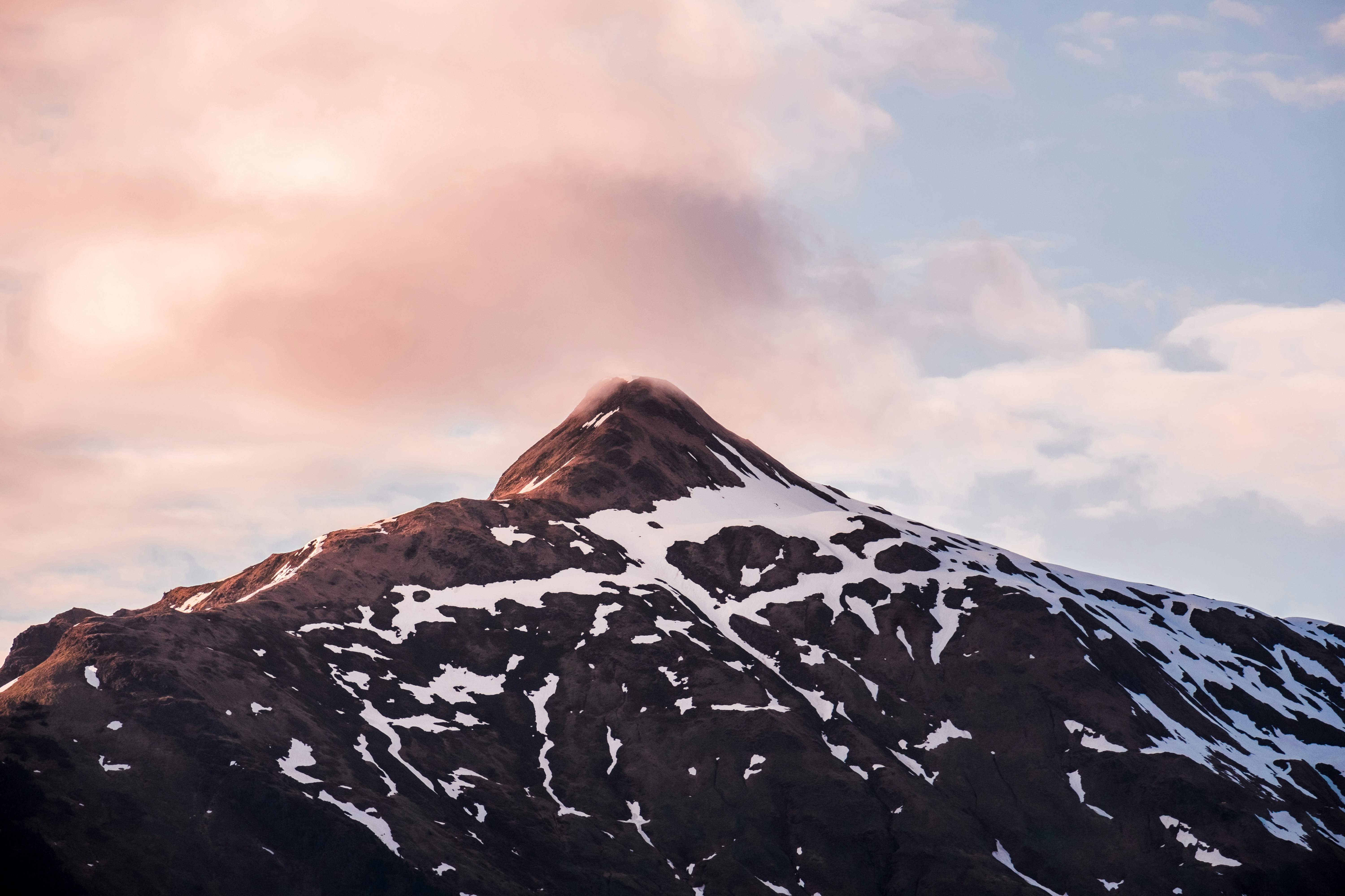 Snow-capped mountain peak piercing through soft clouds during twilight, showcasing the rugged beauty of nature.