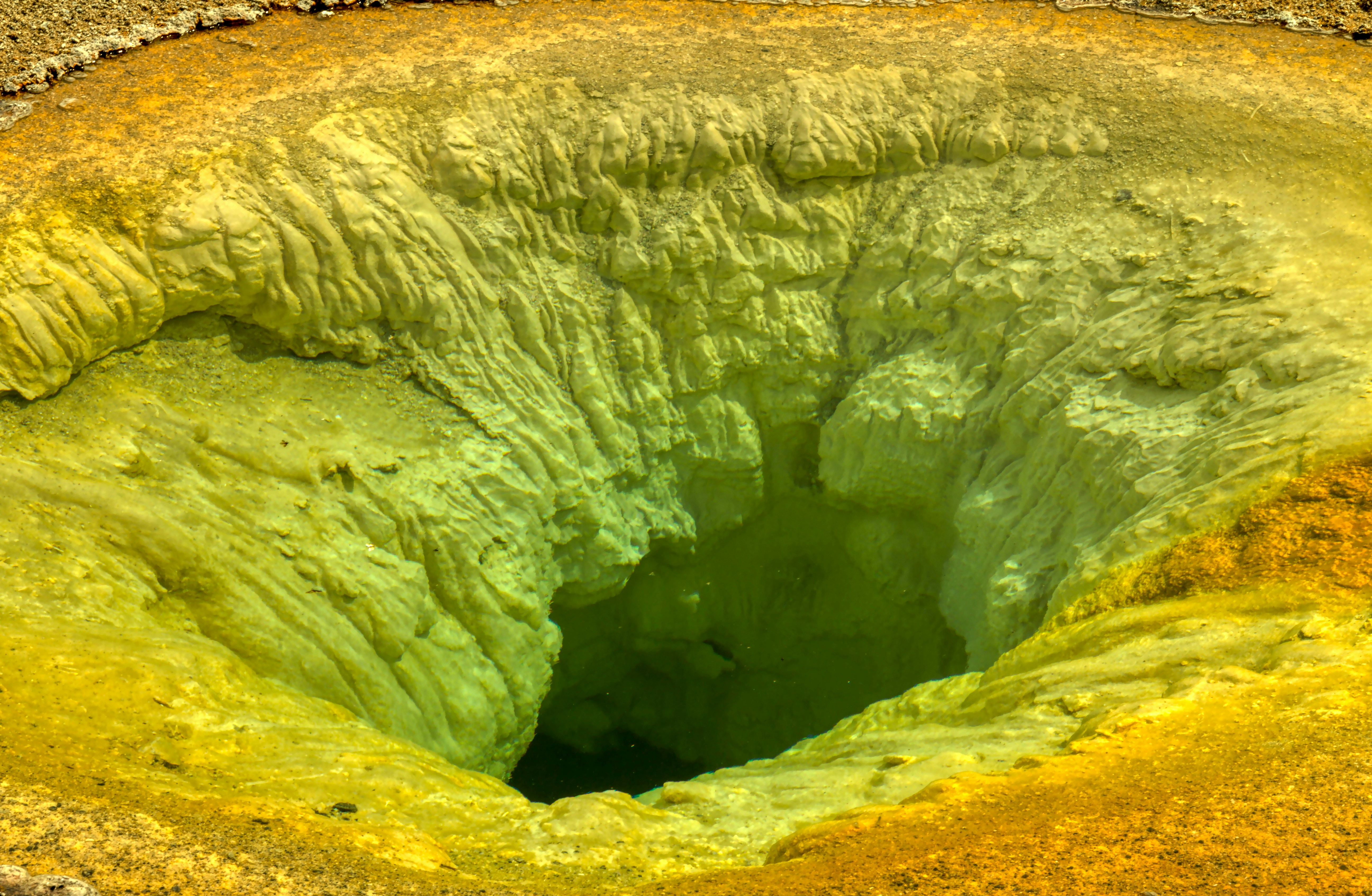 Vivid geothermal pool with textured mineral formations surrounding a deep, greenish-blue center. The unique geological features highlight the beauty of natural thermal activity.